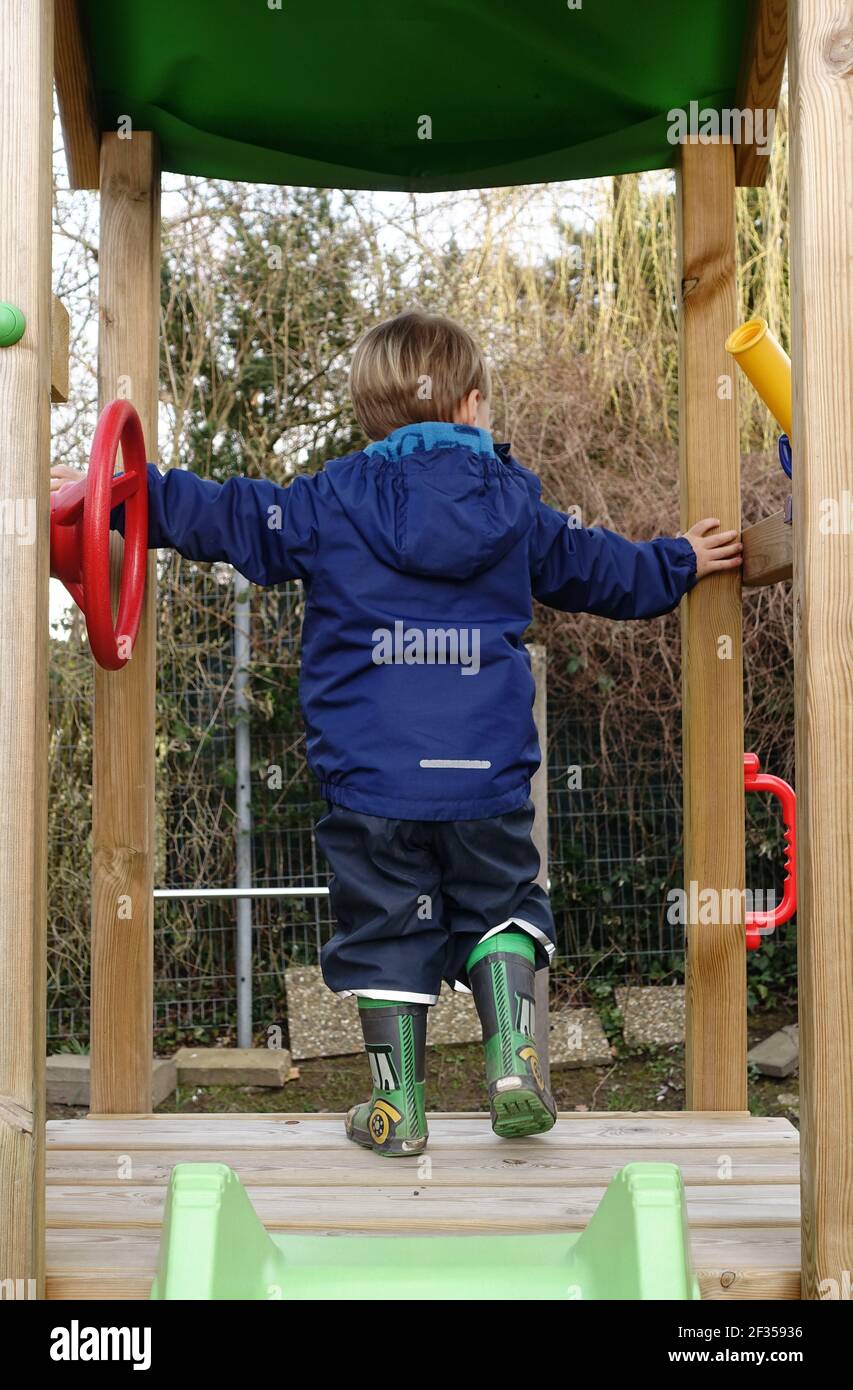 A vertical shot of a cute little boy standing on the climbing frame on ...