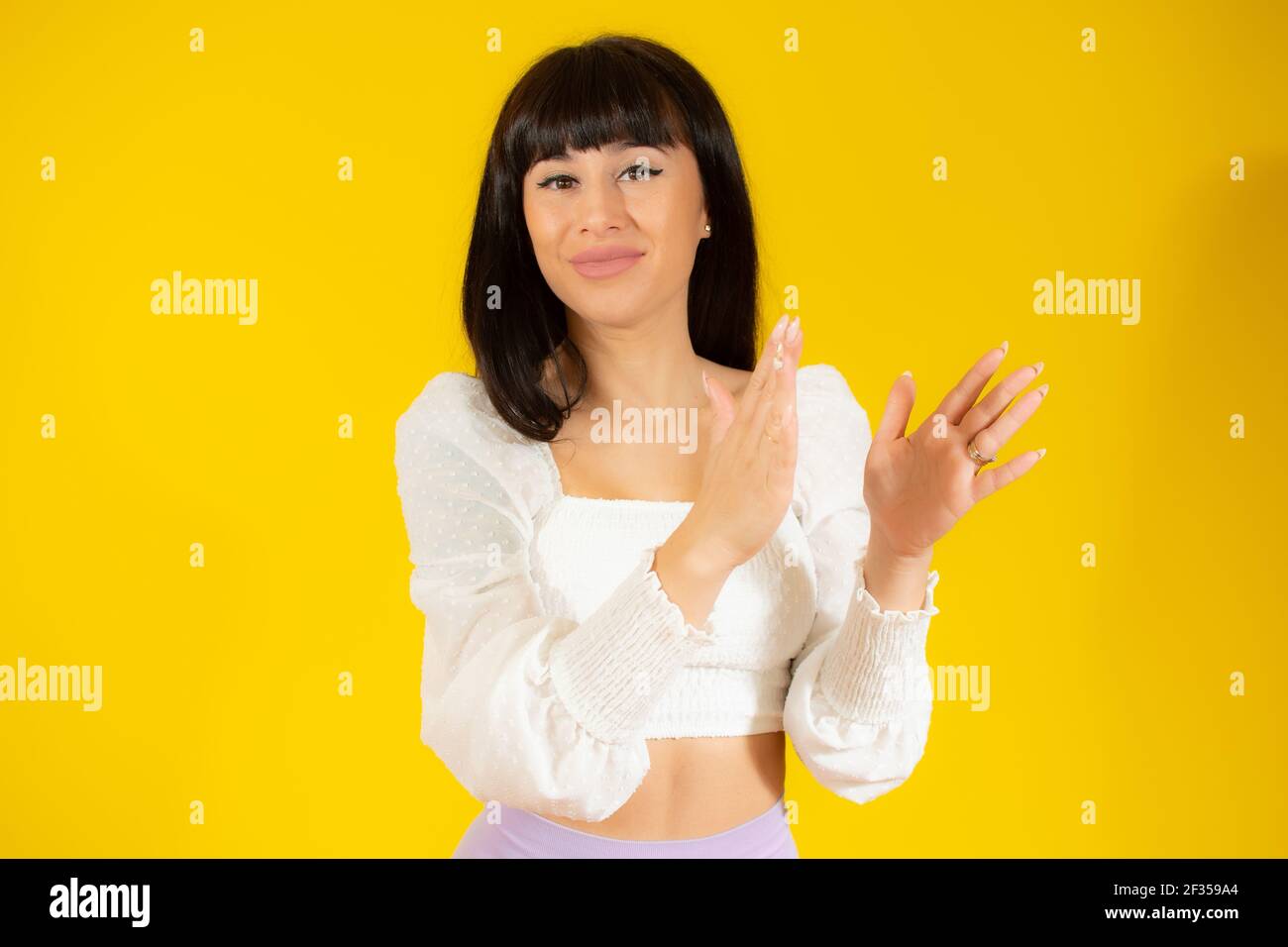 Portrait of young brunette woman clapping hands isolated over yellow ...