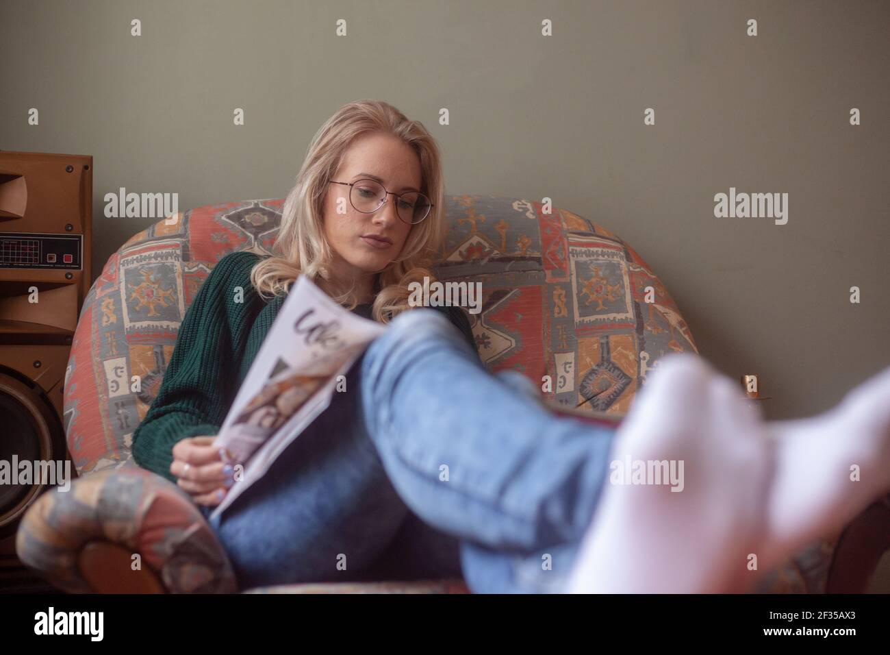 one young woman, flipping pages in magazine, sitting in sofa Stock ...