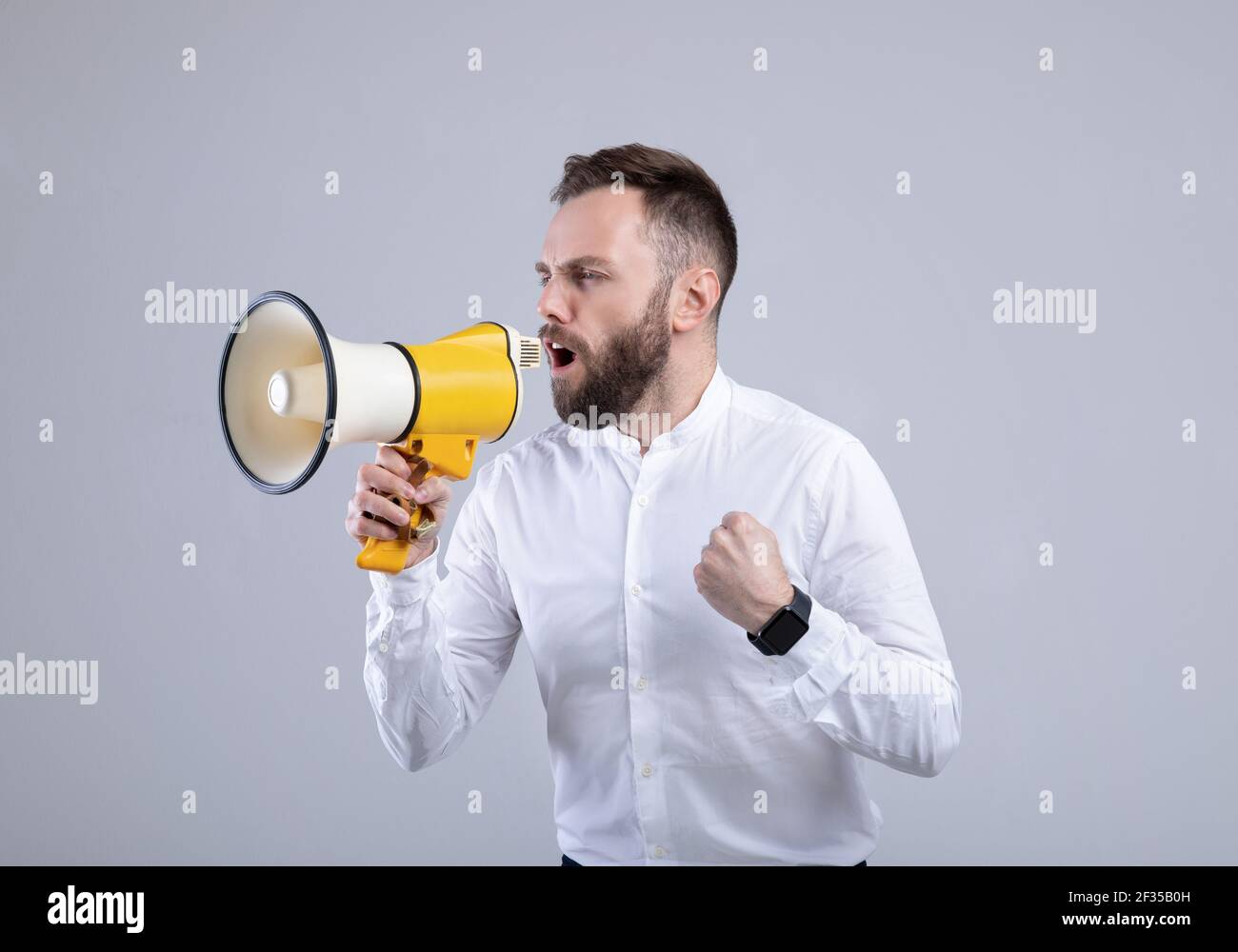 Agitated young man screaming into megaphone on grey studio background ...