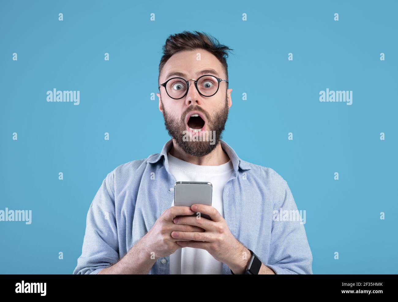 Shocked bearded guy staring at mobile phone in disbelief over blue ...
