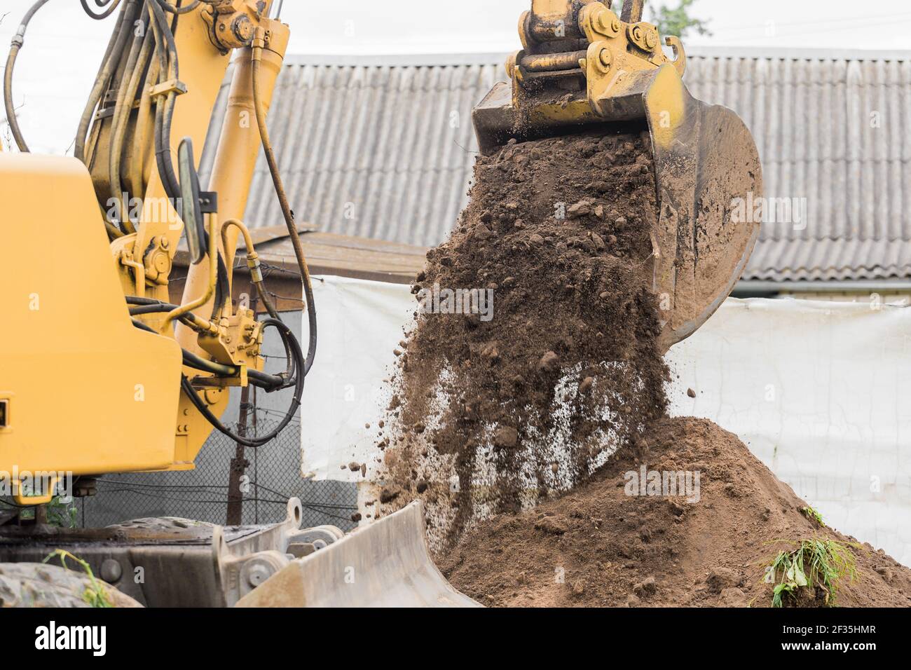 A bucket of excavator pours the ground into a heap against the ...