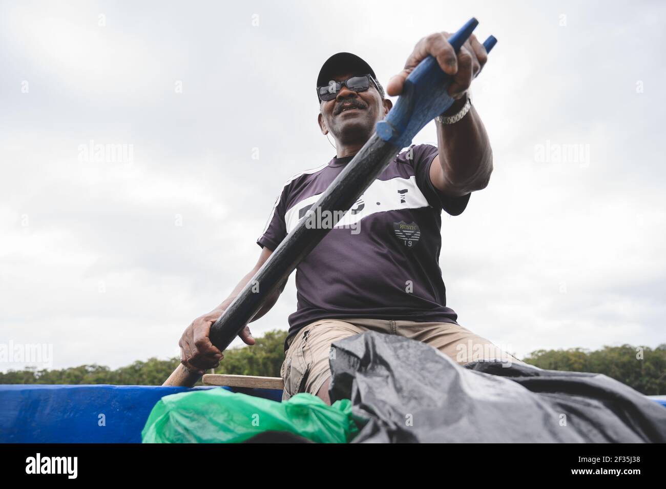 An elderly African-American male with sunglasses and cap rowing a boat ...