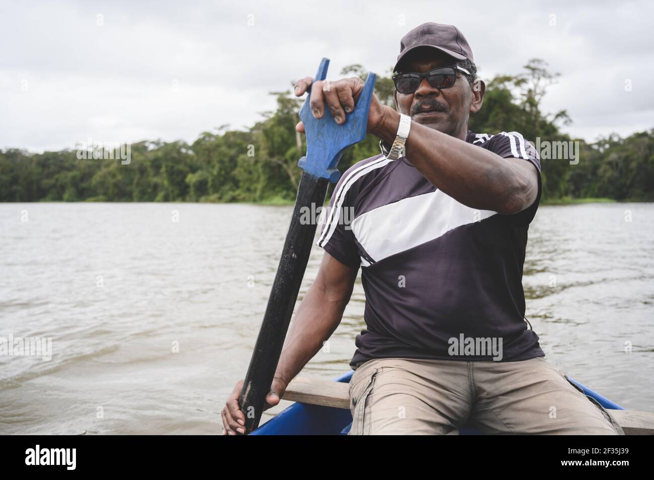 An elderly African-American male with sunglasses and cap rowing a boat ...