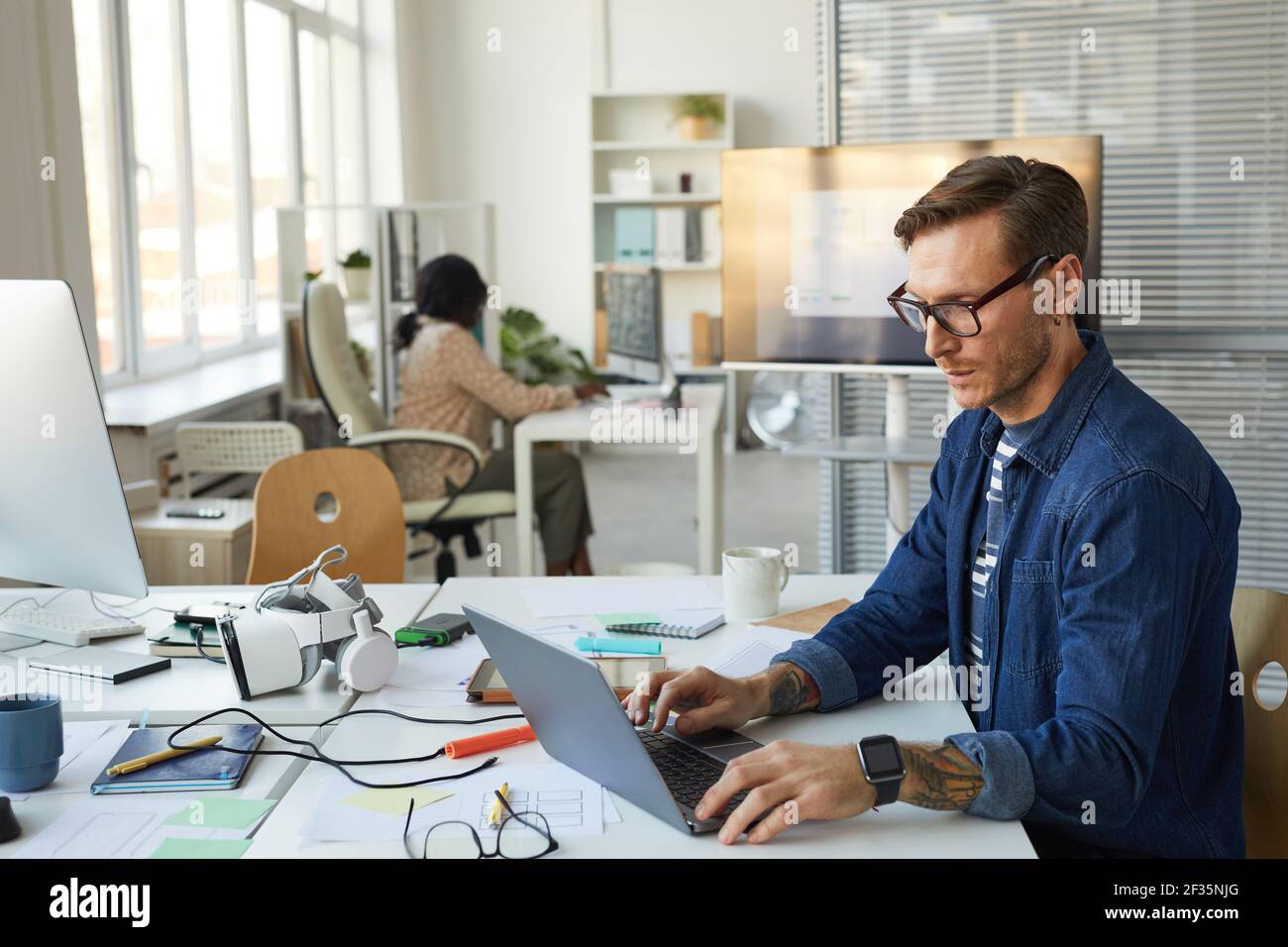 Side view portrait of tattooed IT developer designing VR software while ...