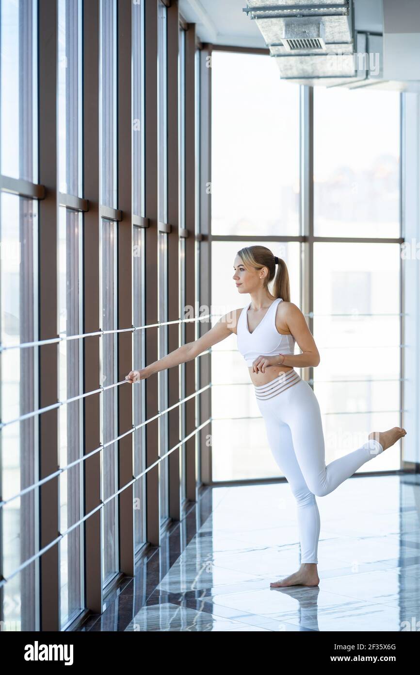 Pretty woman in white sportswear in gymnastics room. Athletic girl ...