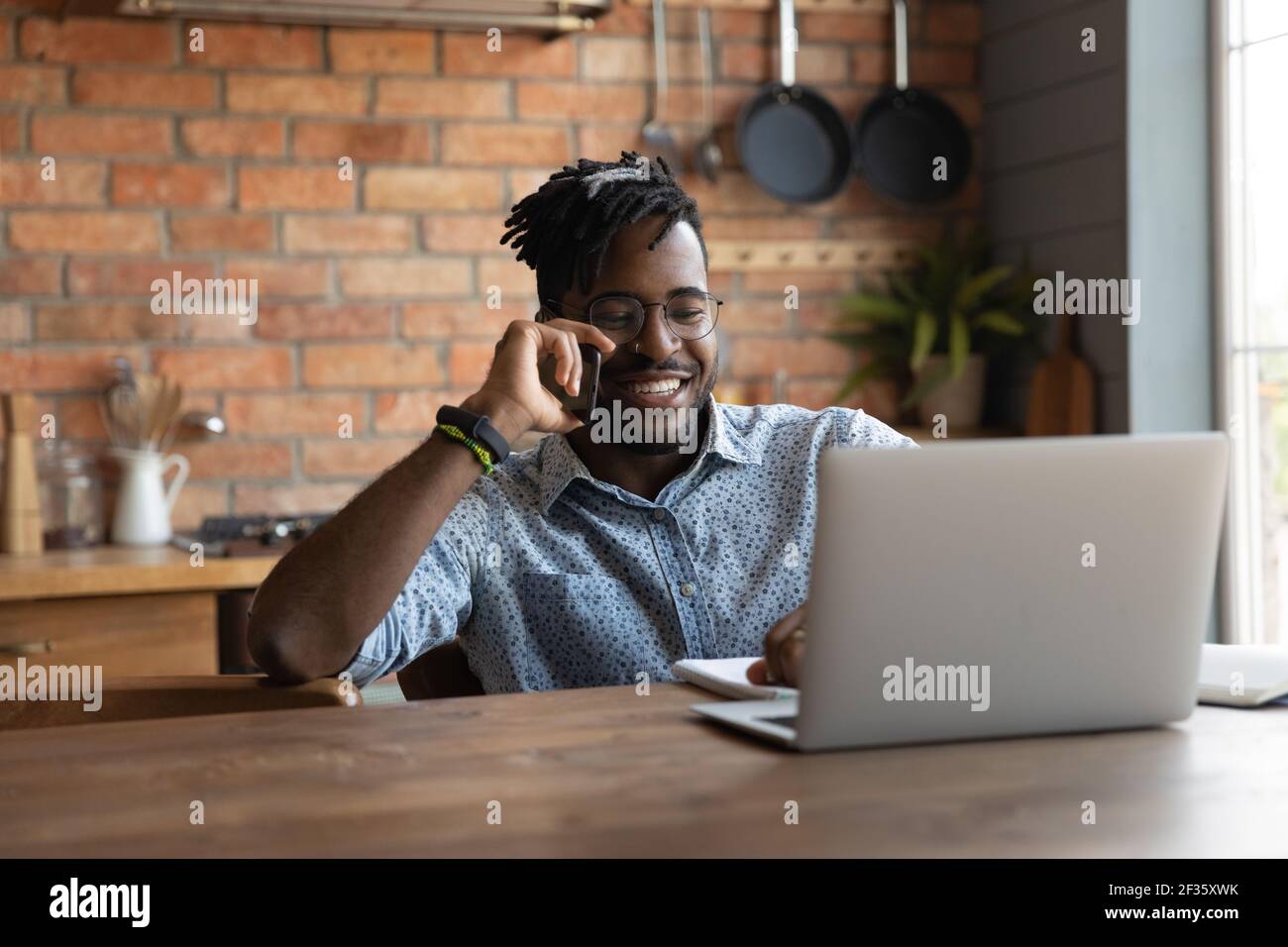 Positive african man answer phone call reading data on laptop Stock ...