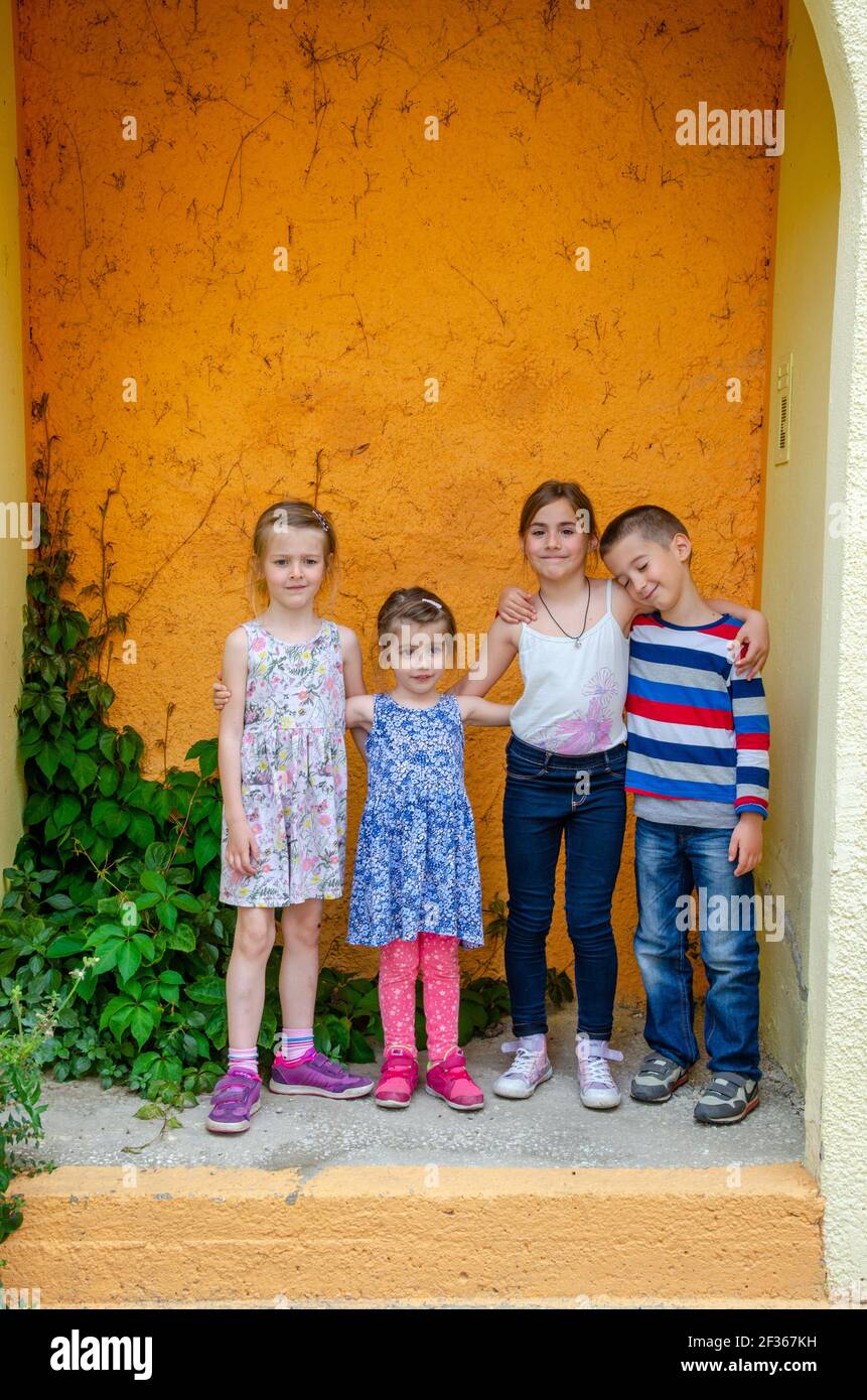 Group of four children smiling on the camera in front of yellow wall ...