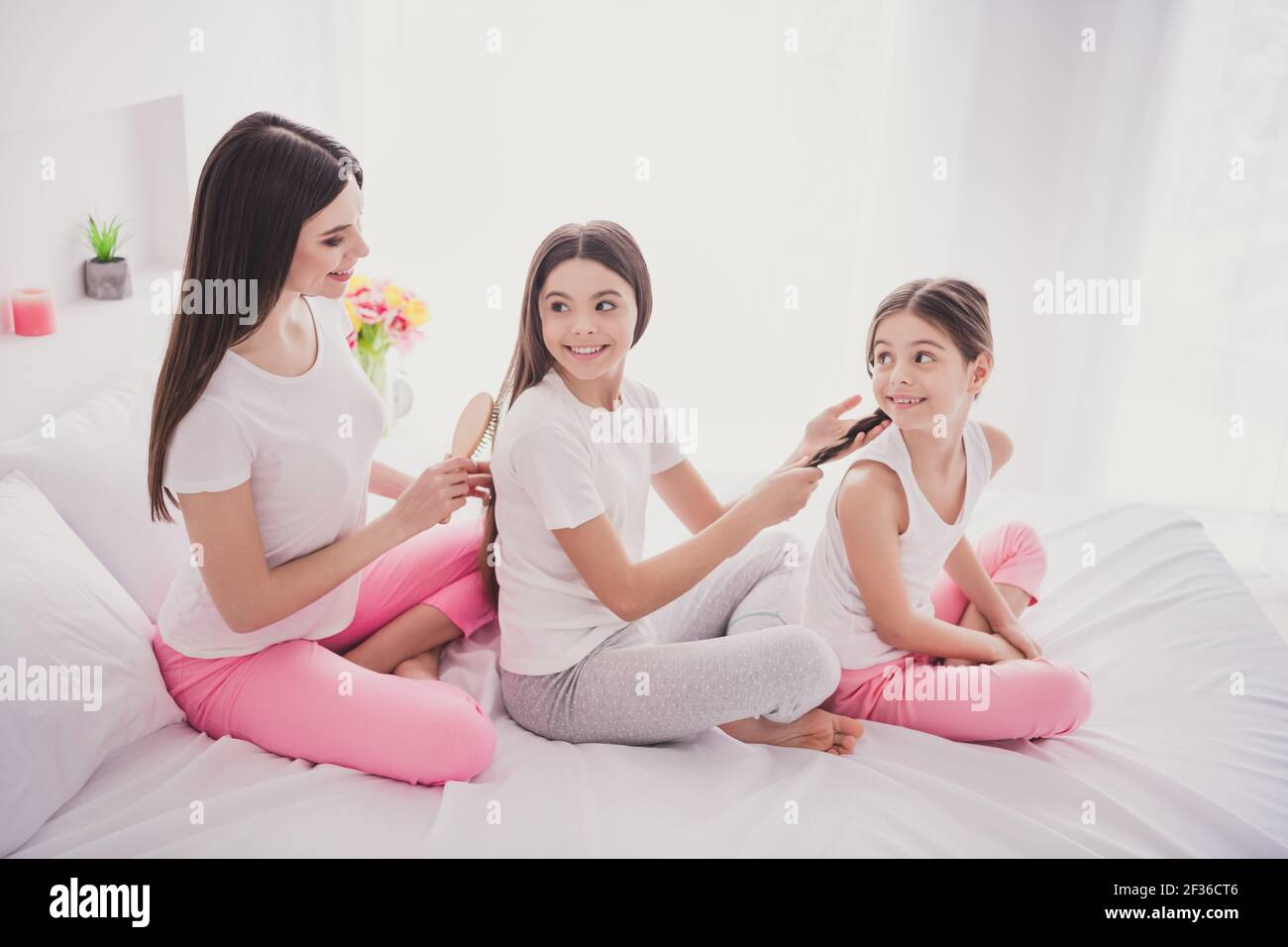 Photo of attractive sweet three siblings nightwear sitting bed brushing ...
