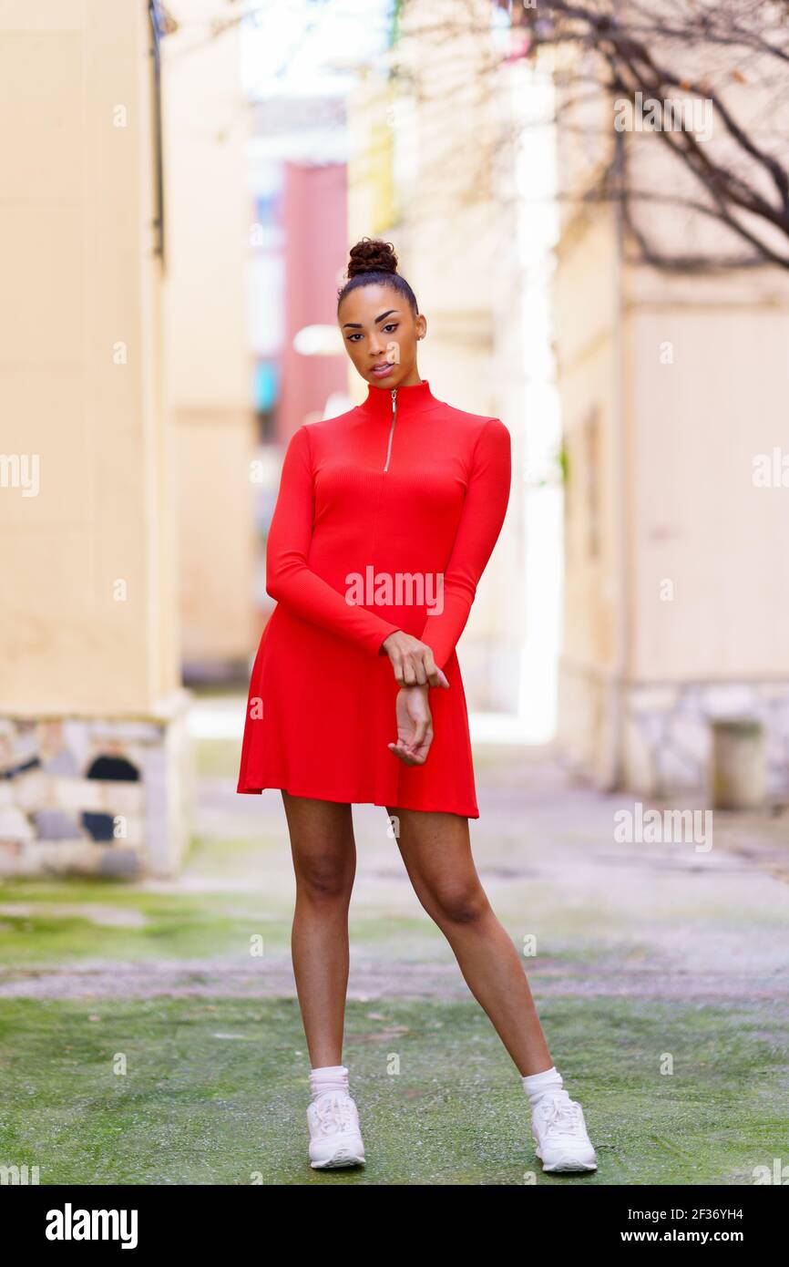 Young mixed woman in red dress posing on a street with colorful walls ...