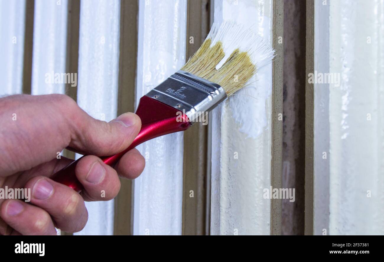 Close-up of a worker's hand painting a heating radiator. Brush in white ...