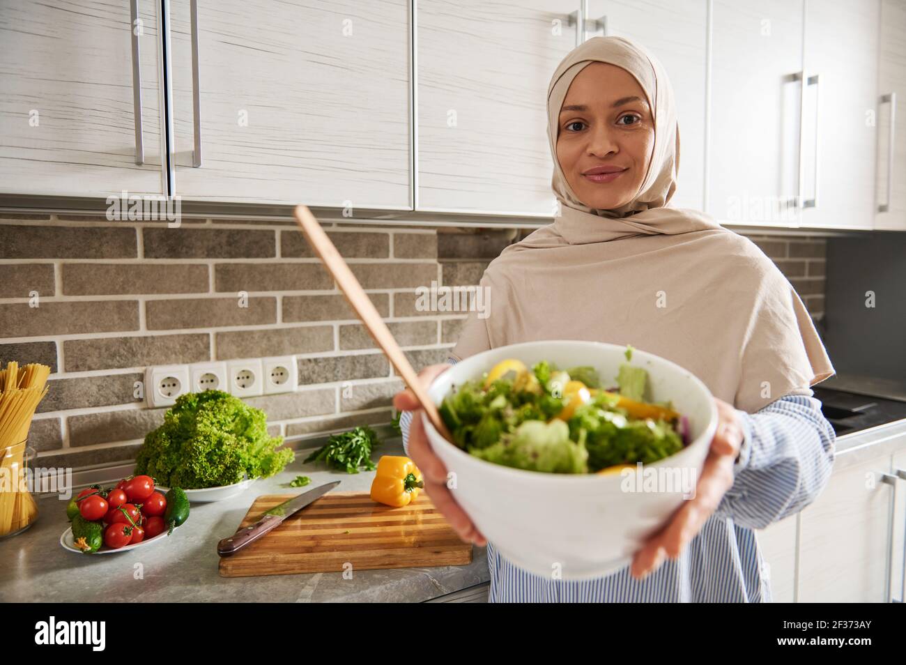 Serene Arab Muslim woman holds a bowl with salad and shows it to the ...