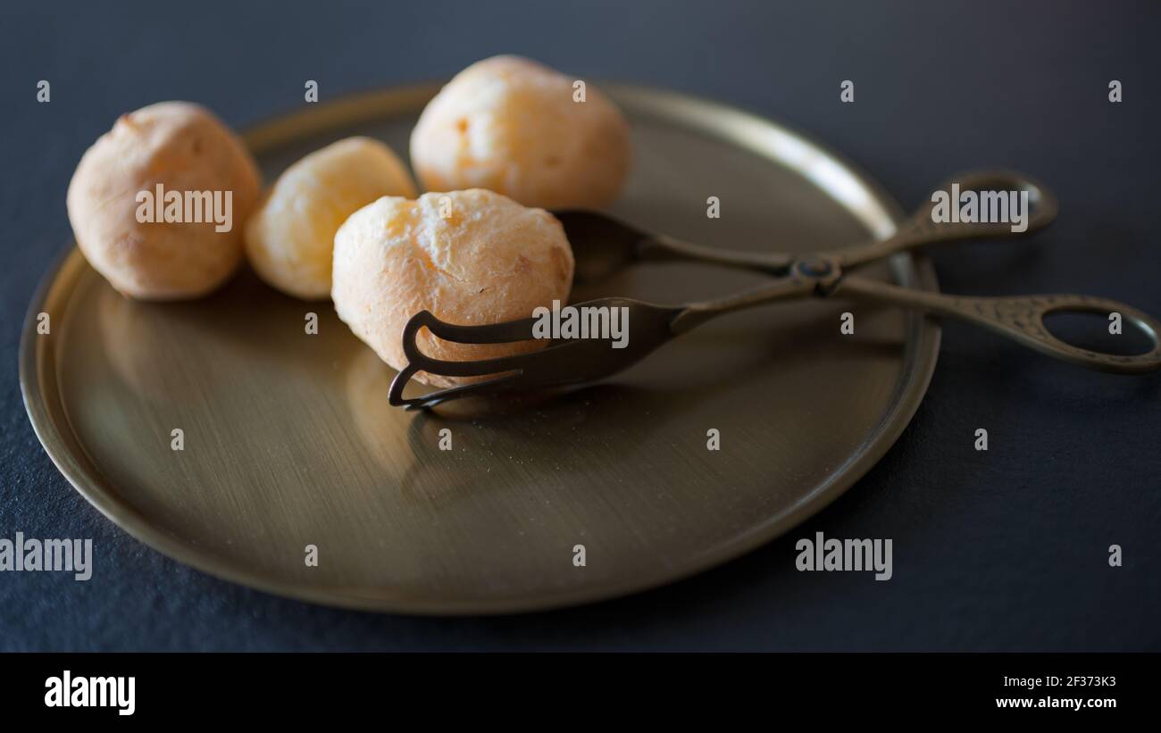Tasty cheese appetizers on a bronze tray and serving tongs. Black ...