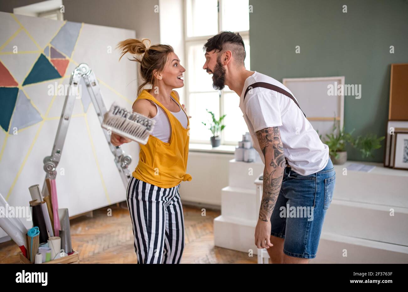 Couple having fun when painting wall indoors at home, relocation and ...