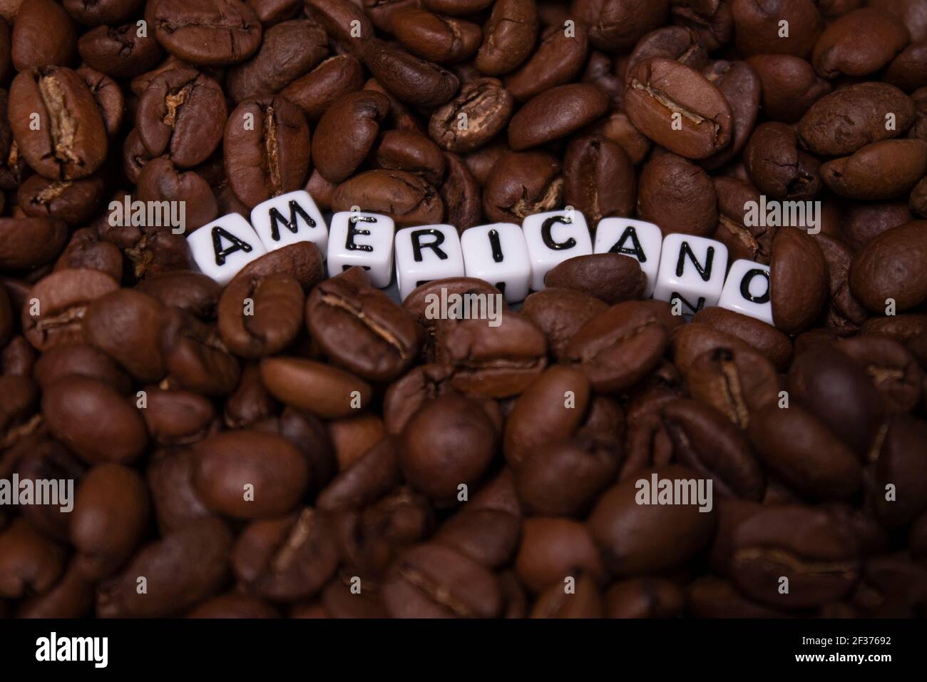 close up of Freshly roasted coffee beans near word AMERICANO written ...