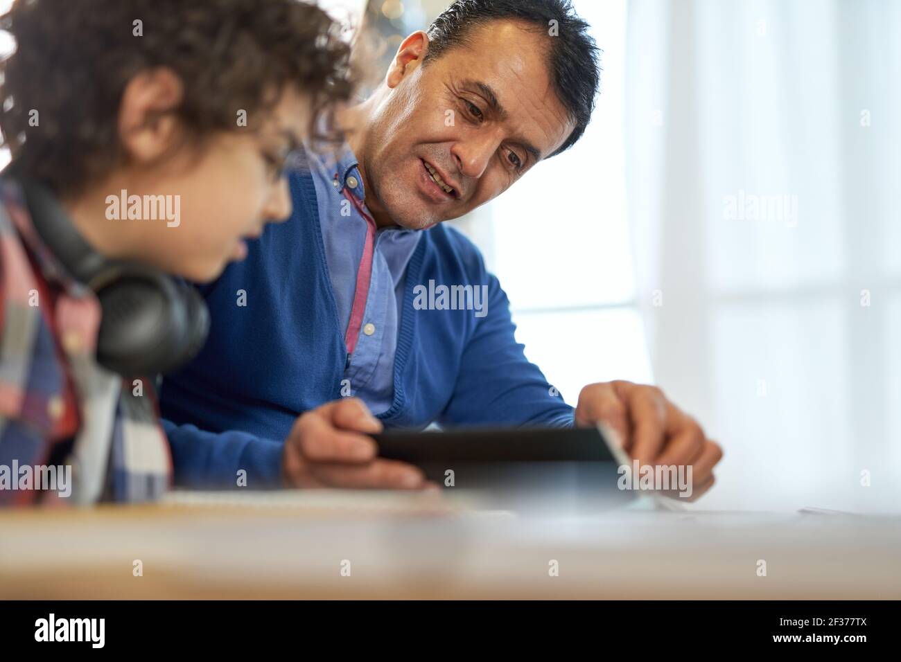 Happy latin middle aged father watching his son, school boy doing his ...