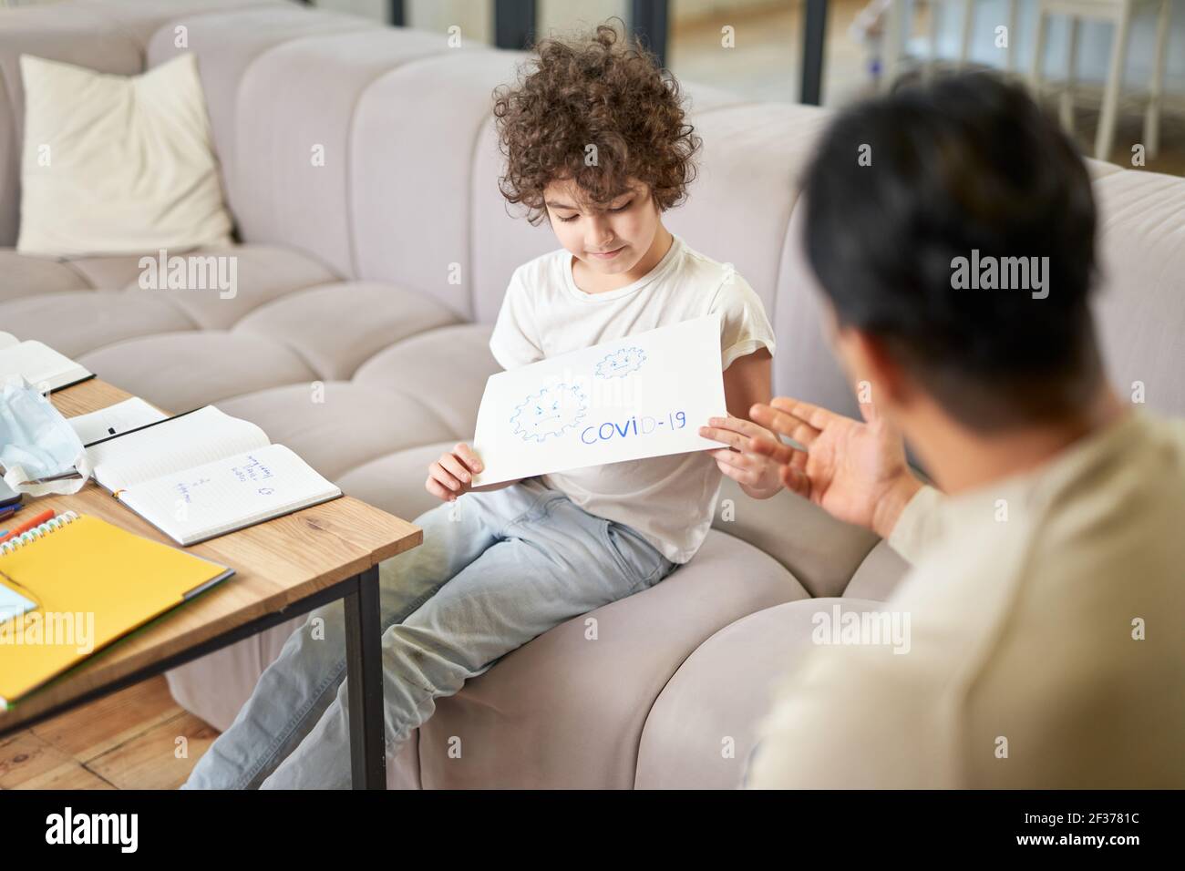 Stay home together. Happy latin boy showing the drawing Covid 19 to his ...