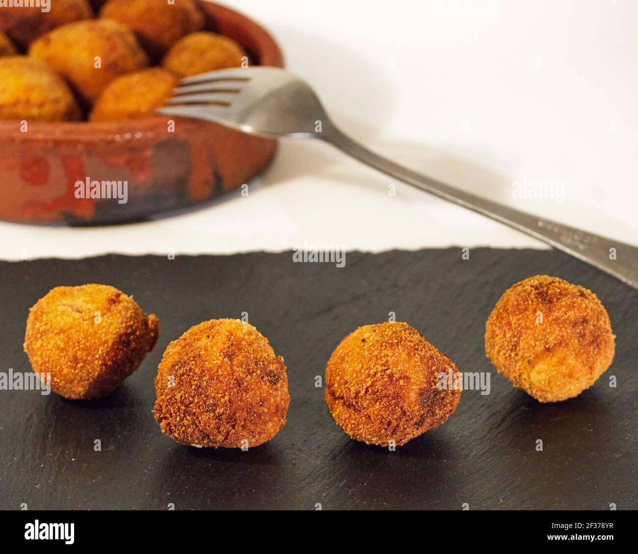 Spanish plate of 4 round croquettes on a black slate board decorated ...