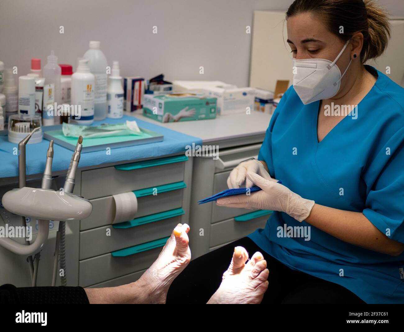 A female podiatrist in a medical mask and gloves treating the feet of a ...