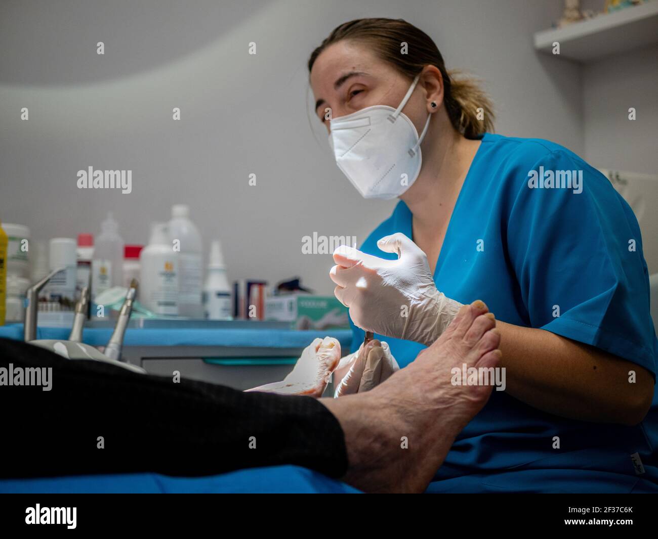 A female podiatrist in a medical mask and gloves treating the feet of a ...