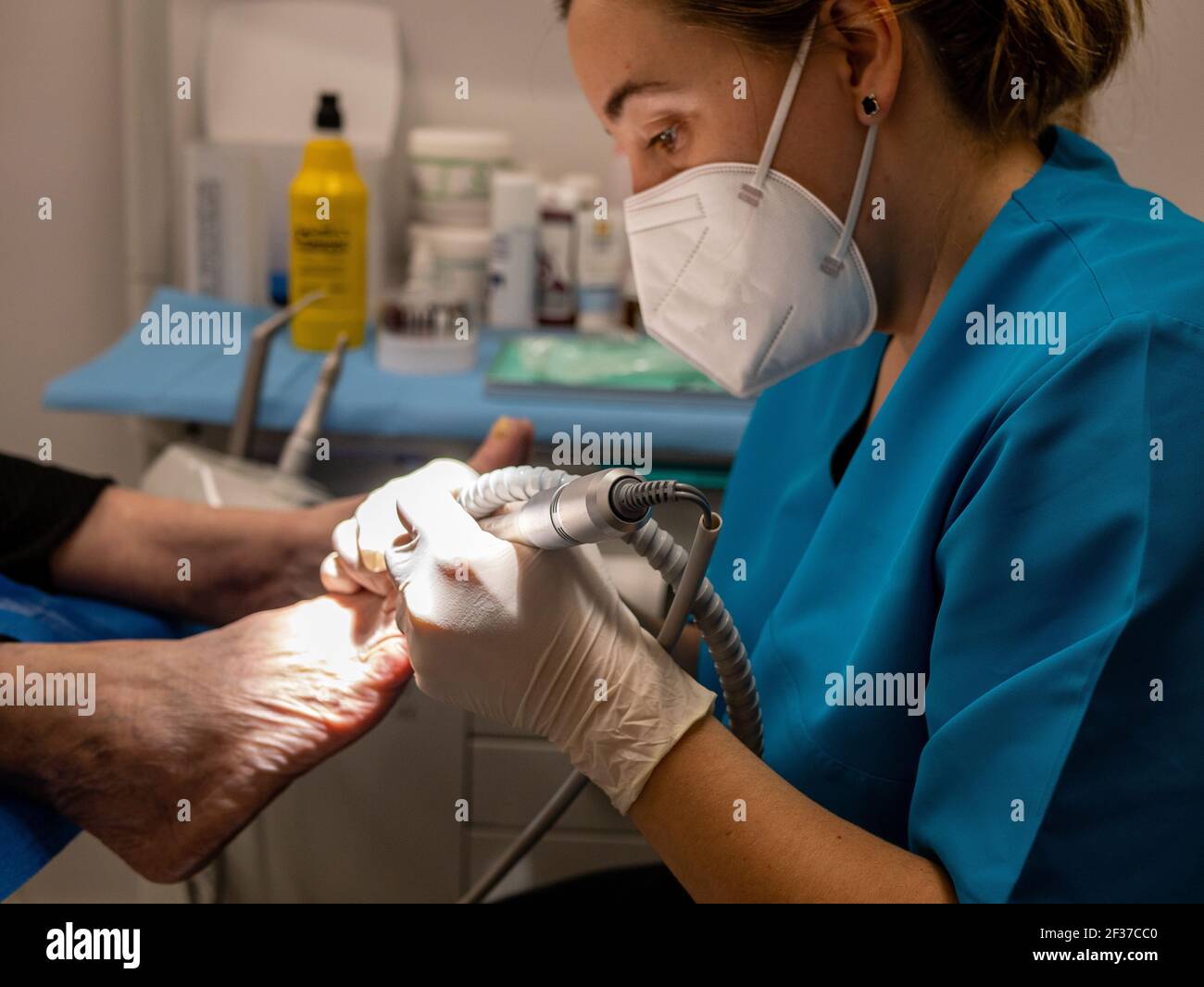 A female podiatrist in a medical mask and gloves treating the feet of a ...