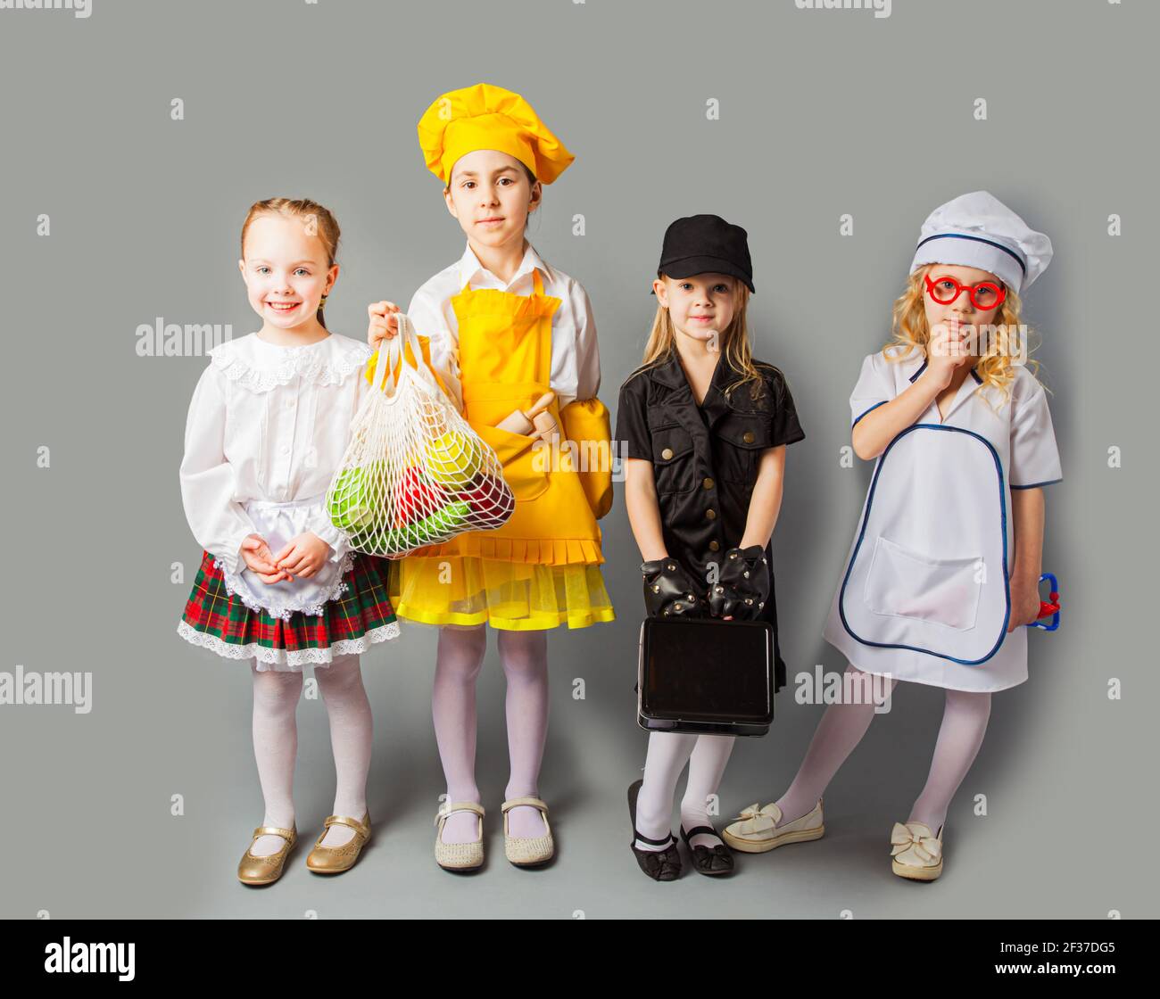 Happy schoolgirls in costumes of different professions isolated on grey ...