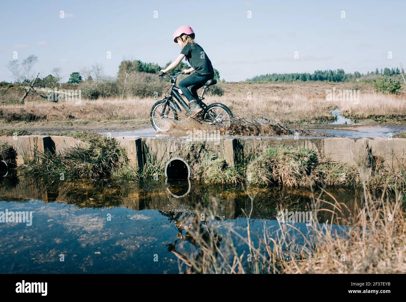 young girl on her bike riding through a big puddle splashing Stock ...
