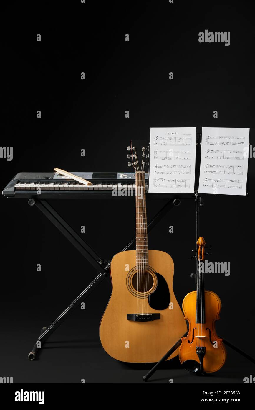 Note stand with music sheets and different musical instruments on dark ...