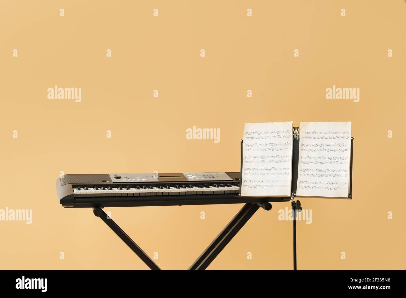 Note stand with music sheets and synthesizer on color background Stock ...