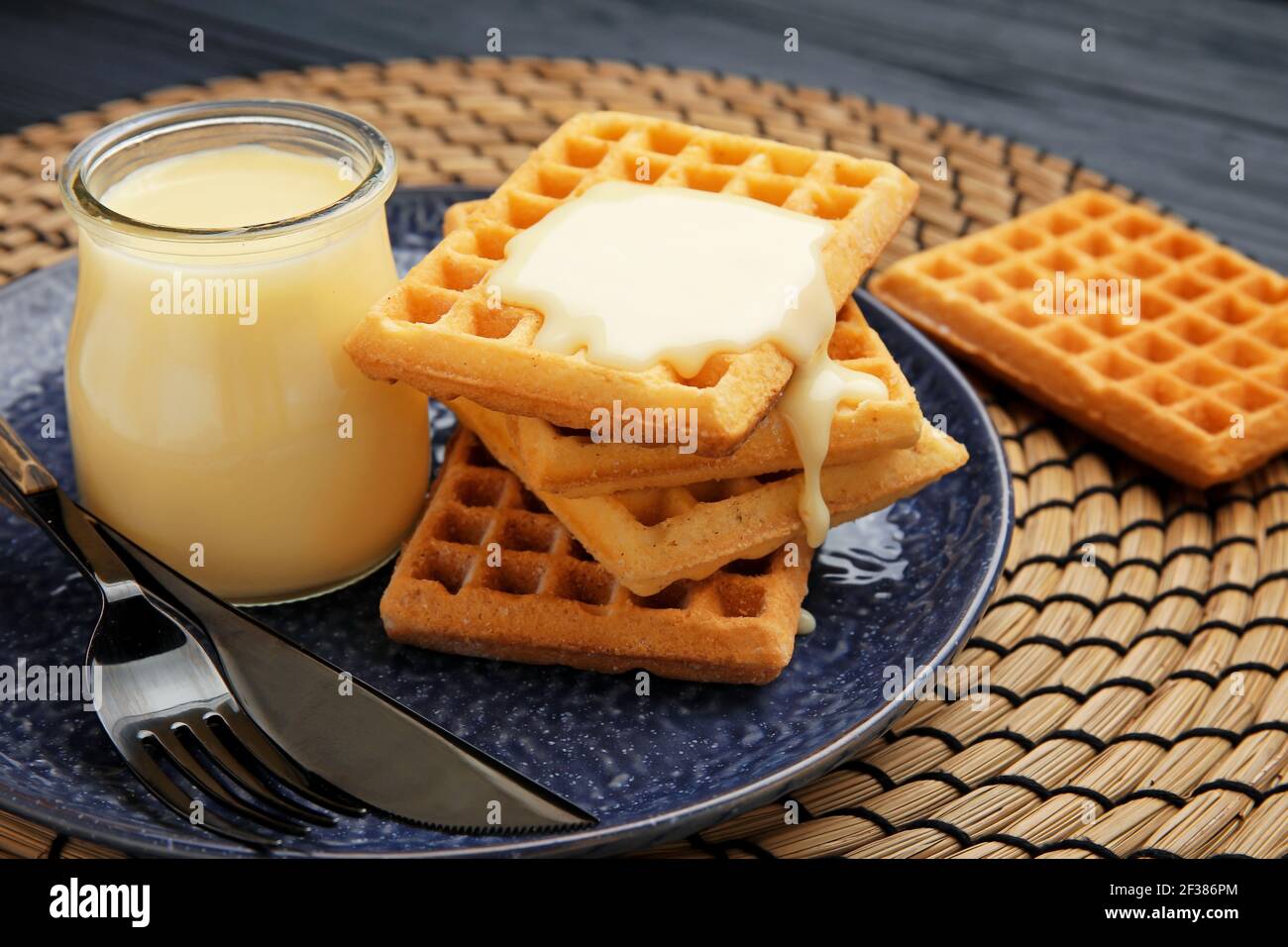 Jar with sweet condensed milk and waffles on table Stock Photo - Alamy