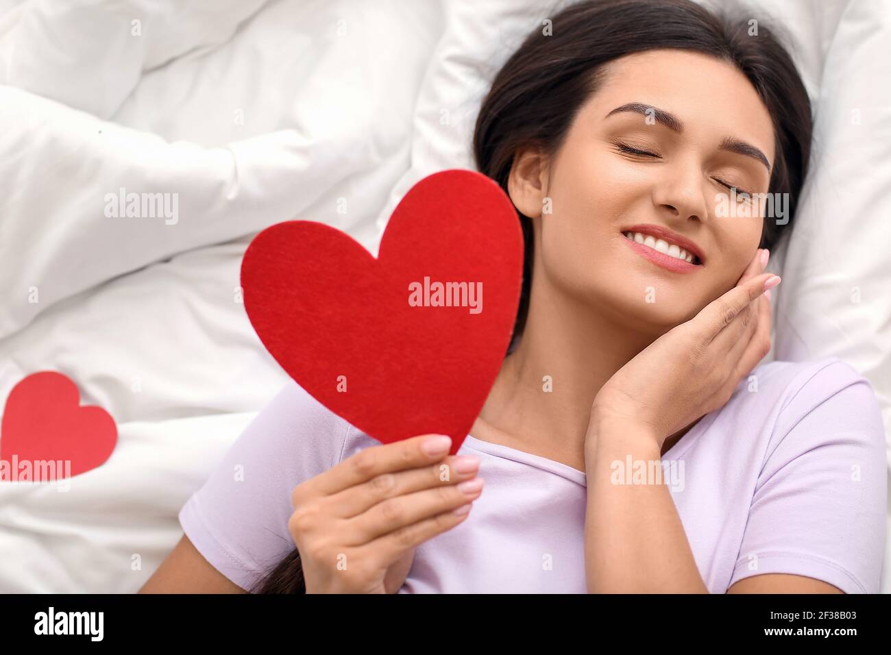 Beautiful young woman with red heart in bed Stock Photo - Alamy