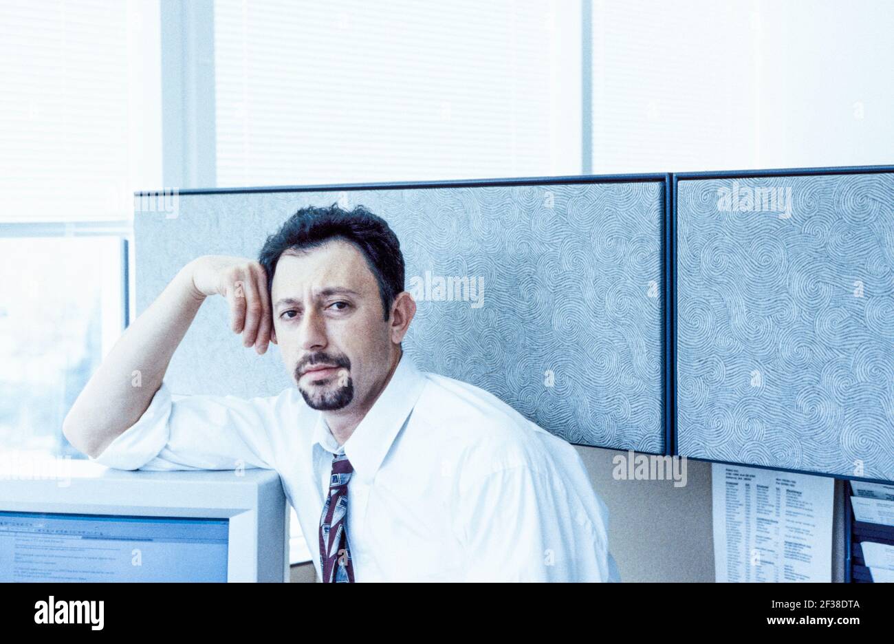 Businessman leaning up against his computer monitor in the office. 1990 ...