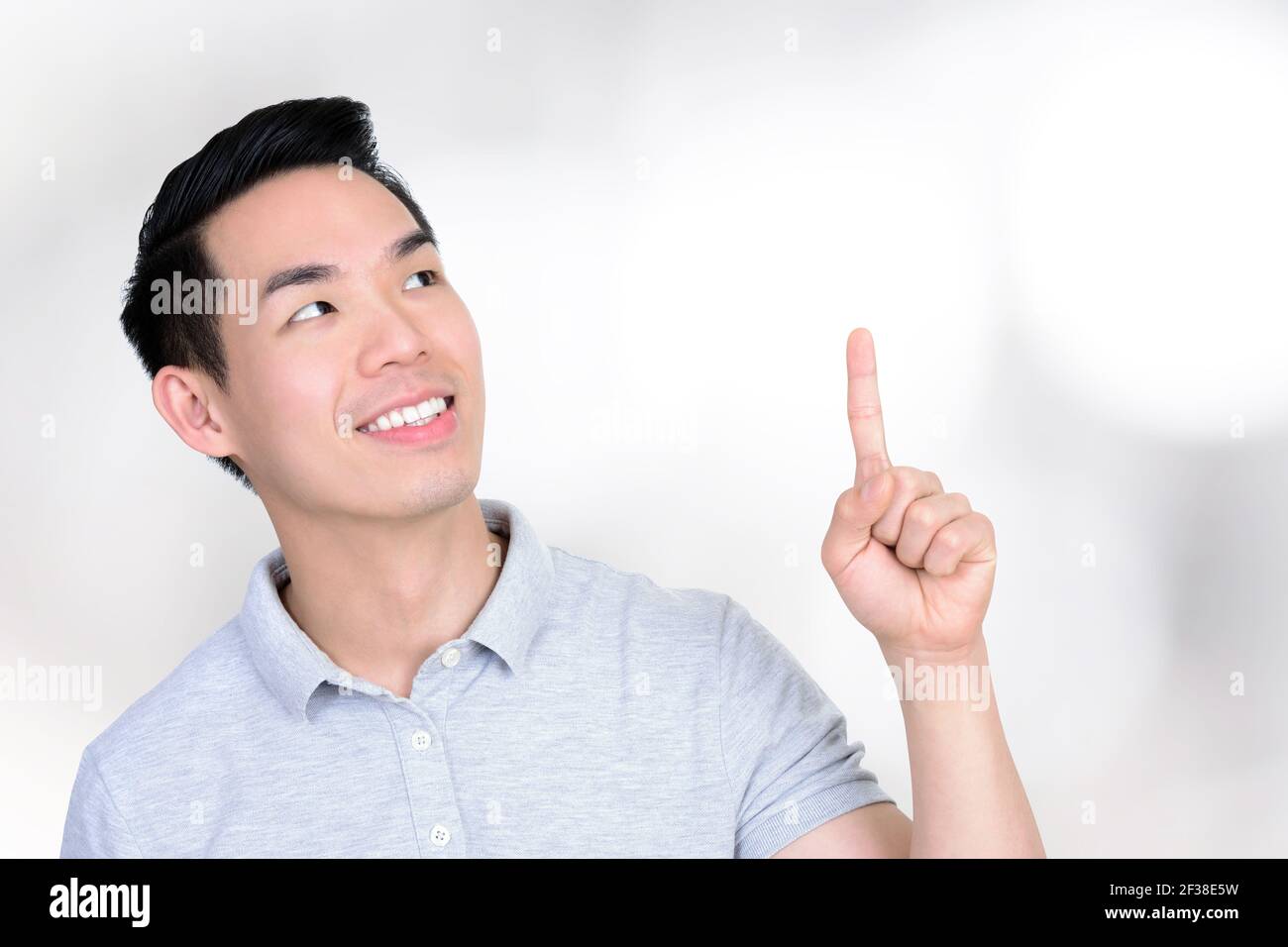Smiling young Asian man looking and pointing up, on blur white gray ...