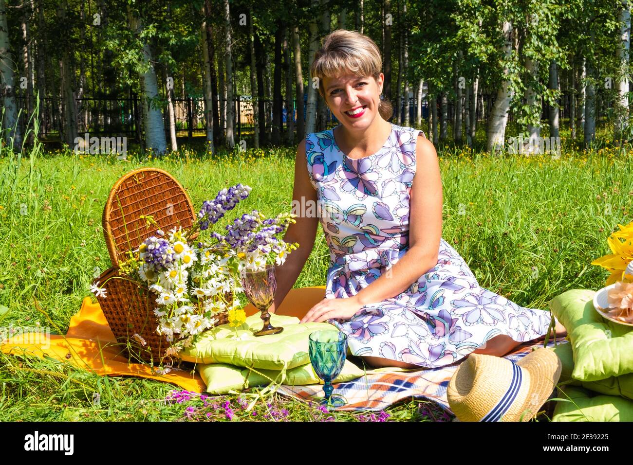 Gorgeous young girl in a sundress lying on grass and having a picnic in ...