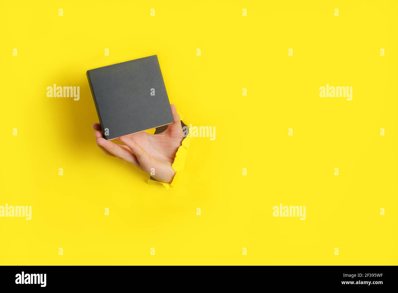 woman hand holding small dark grey box through the hole in yellow paper ...