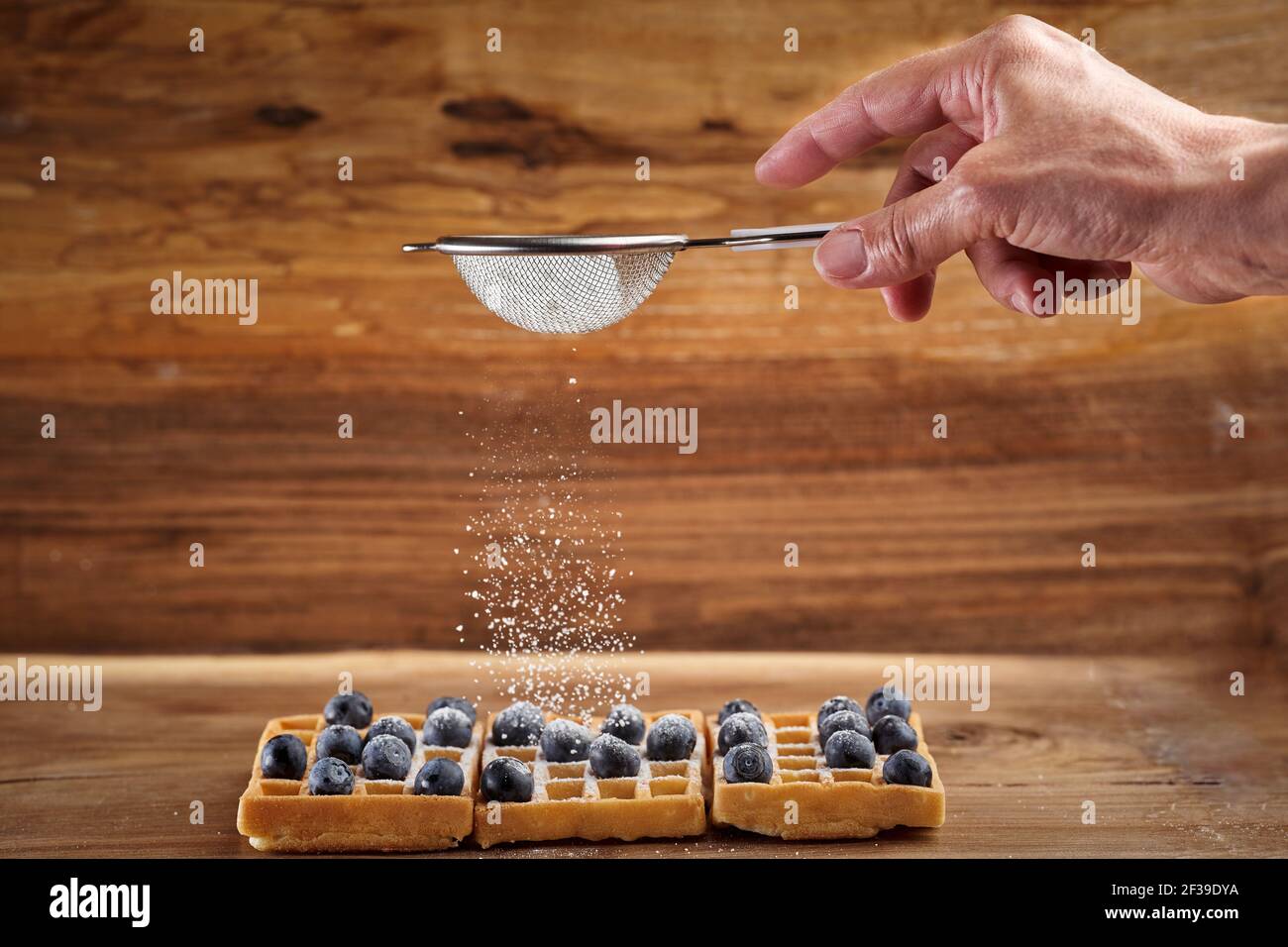 Woman's hand sprinkling powder sugar on waffles with blueberries Stock ...