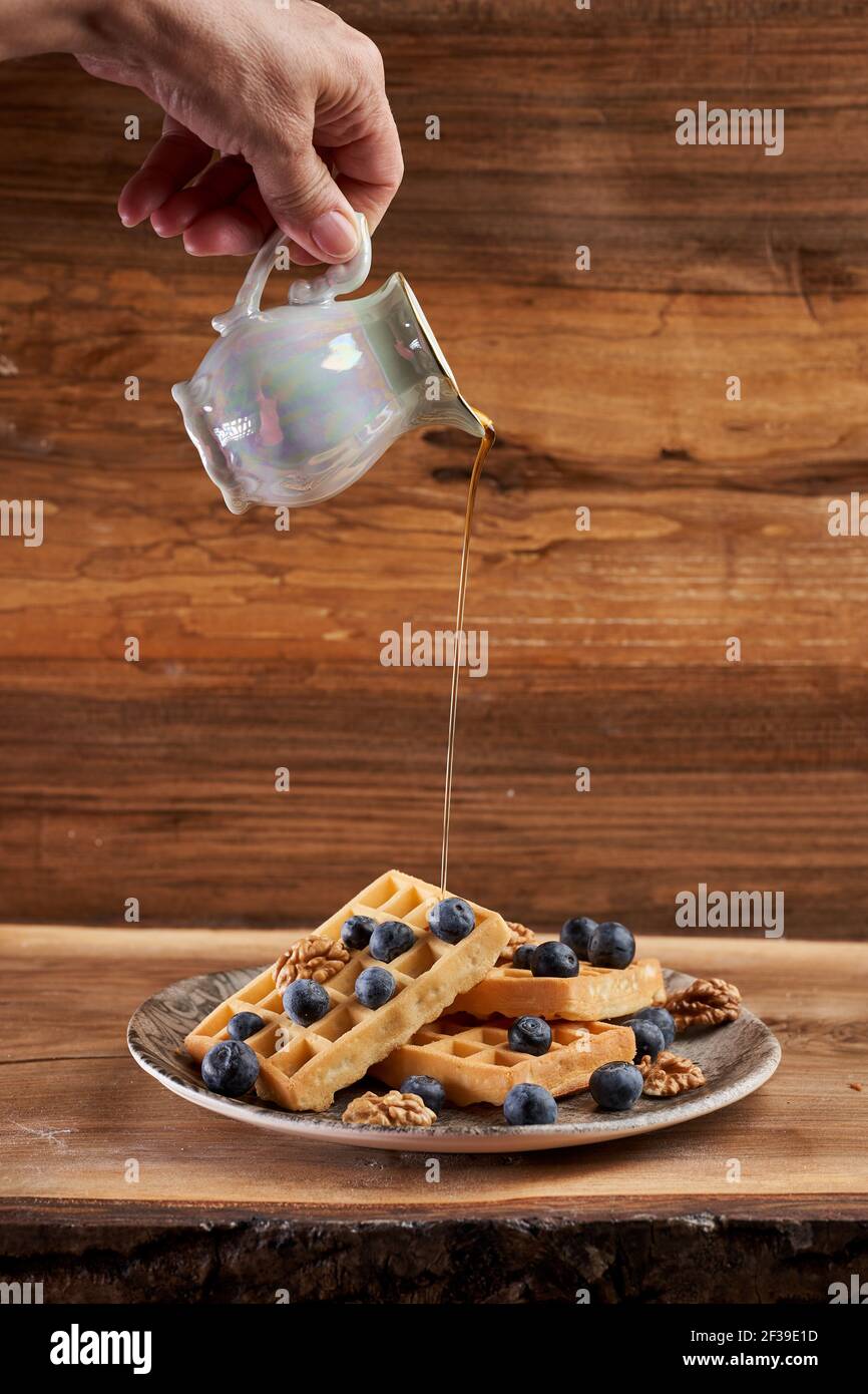Pouring maple syrup on waffles with blueberries and walnuts Stock Photo ...