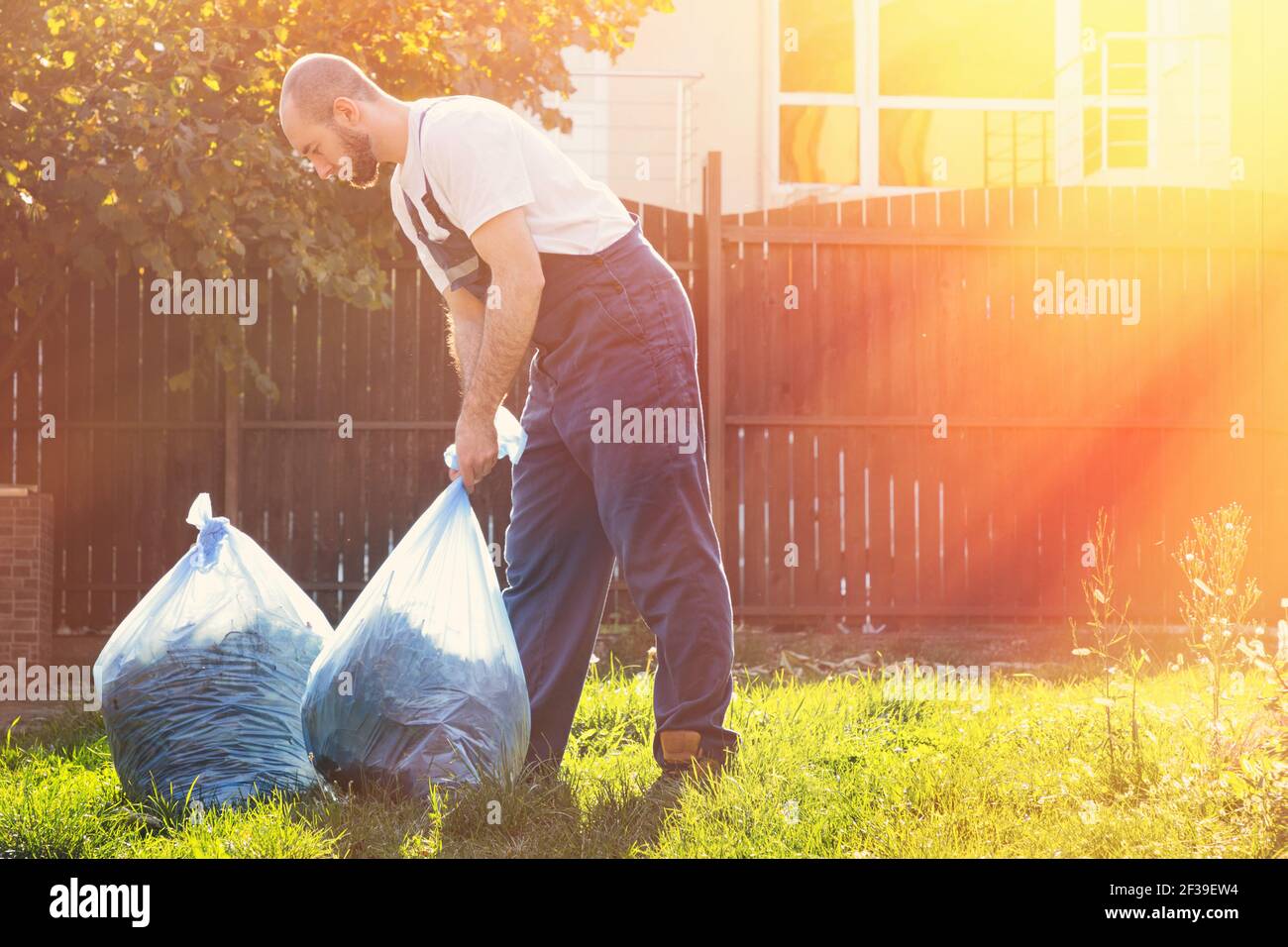 A man in a blue uniform finishes cleaning at sunset , collecting bags ...
