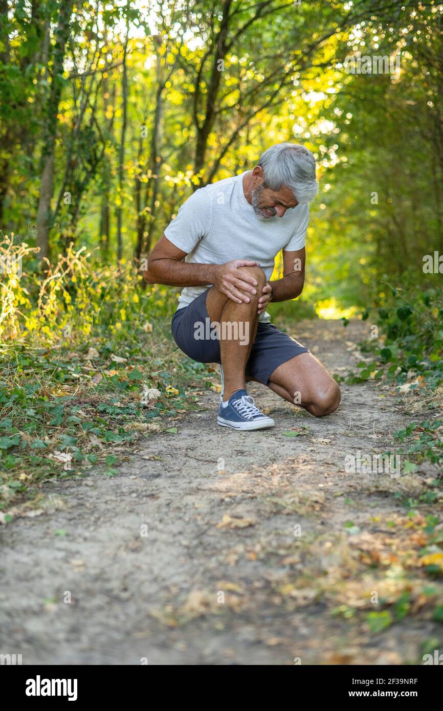 Mature man suffering from knee pain while crouching in forest Stock ...