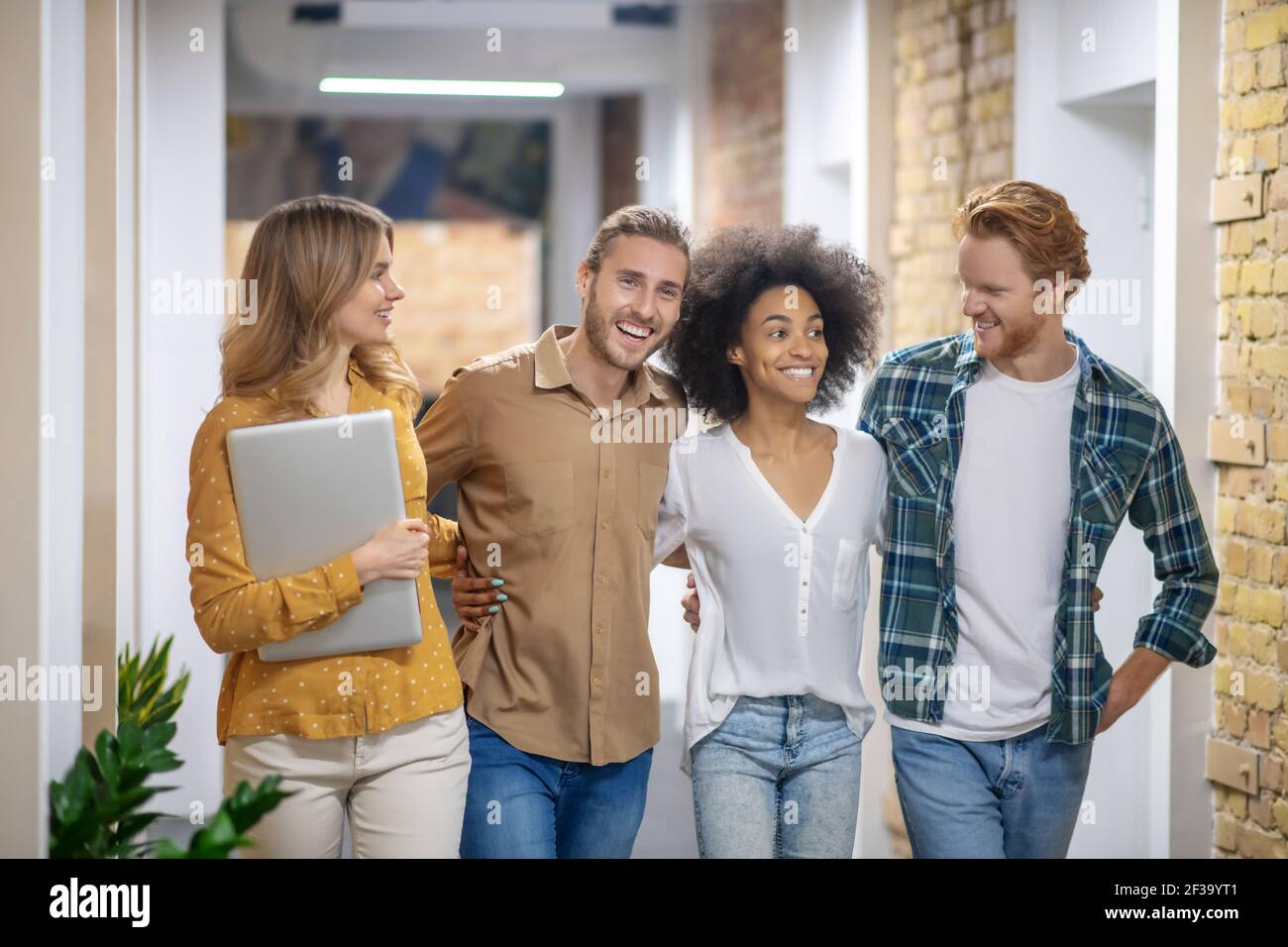 Good friends. Group of smiling young people walking in the corridor and ...
