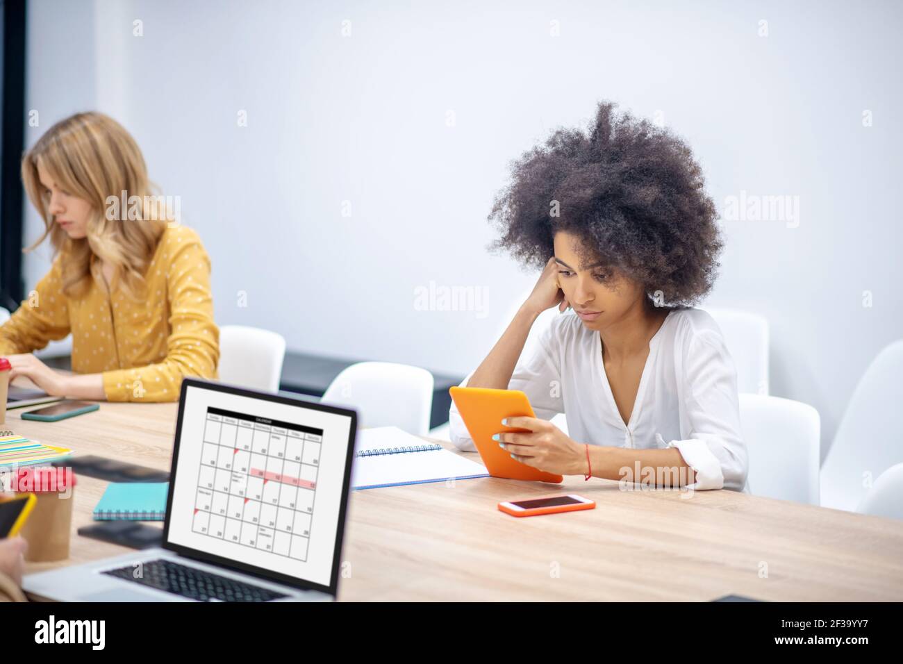 Busy girls. Two girls sitting at the tables in the office and looking ...