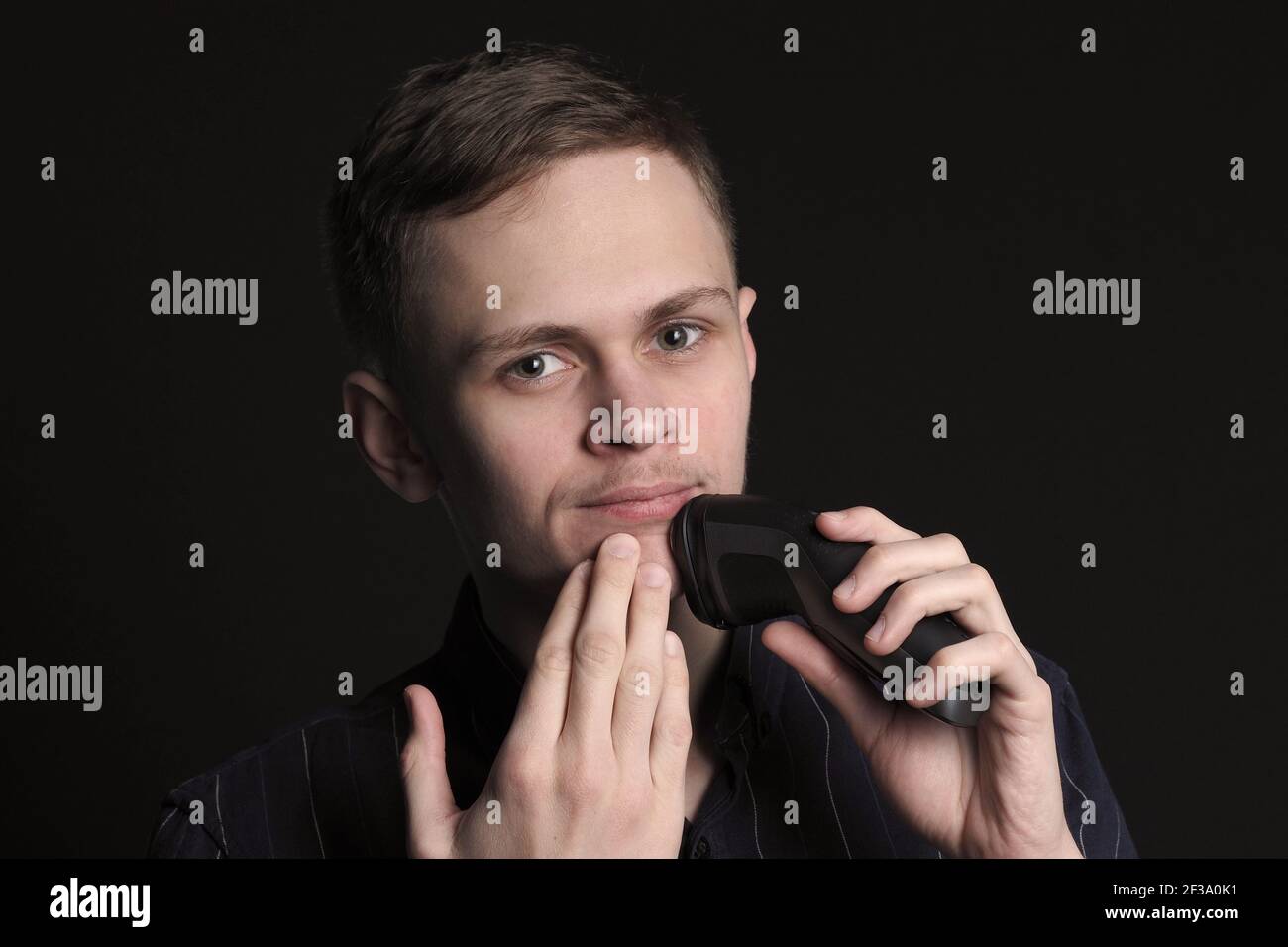Shave safely. A young man shaves his face with an electric razor Stock ...