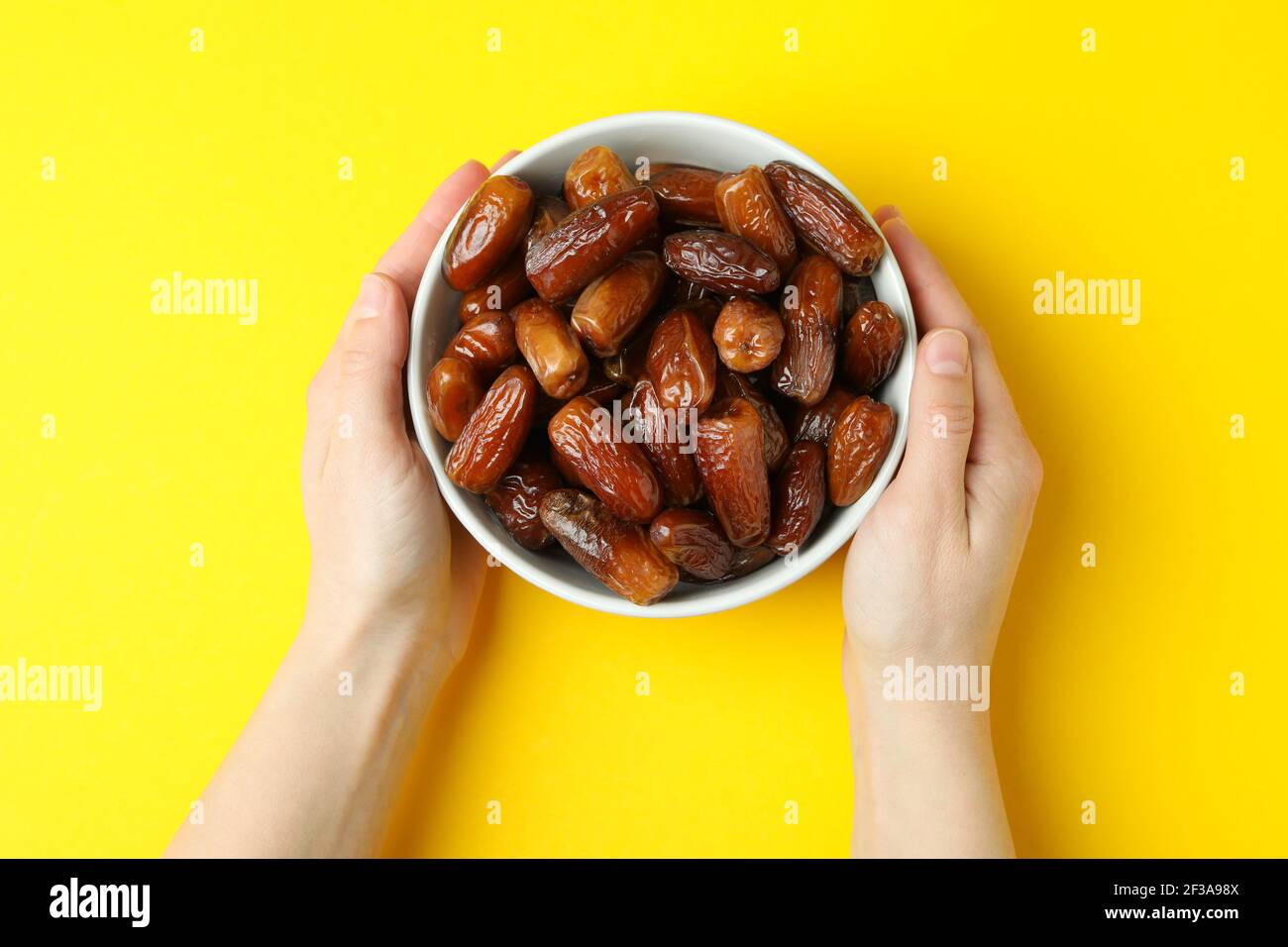 Female hands hold bowl of dried dates on yellow background Stock Photo ...