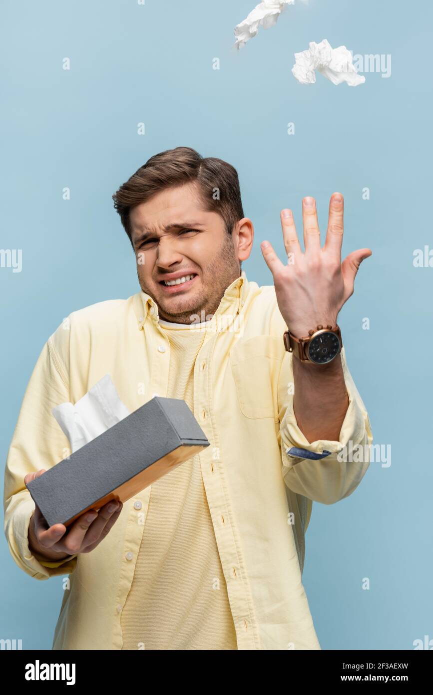 sick man throwing away napkins and holding tissue box isolated on blue ...