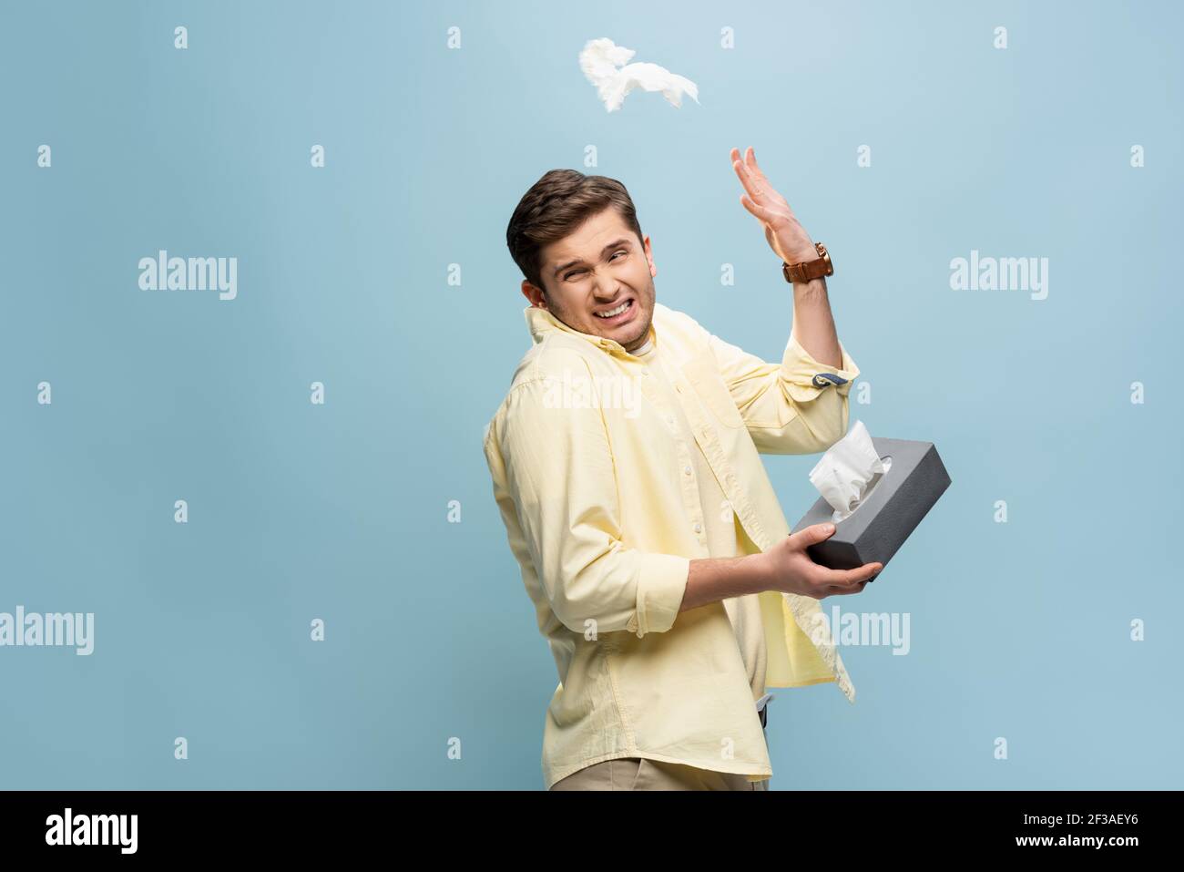 sick man throwing away napkin and holding tissue box isolated on blue ...