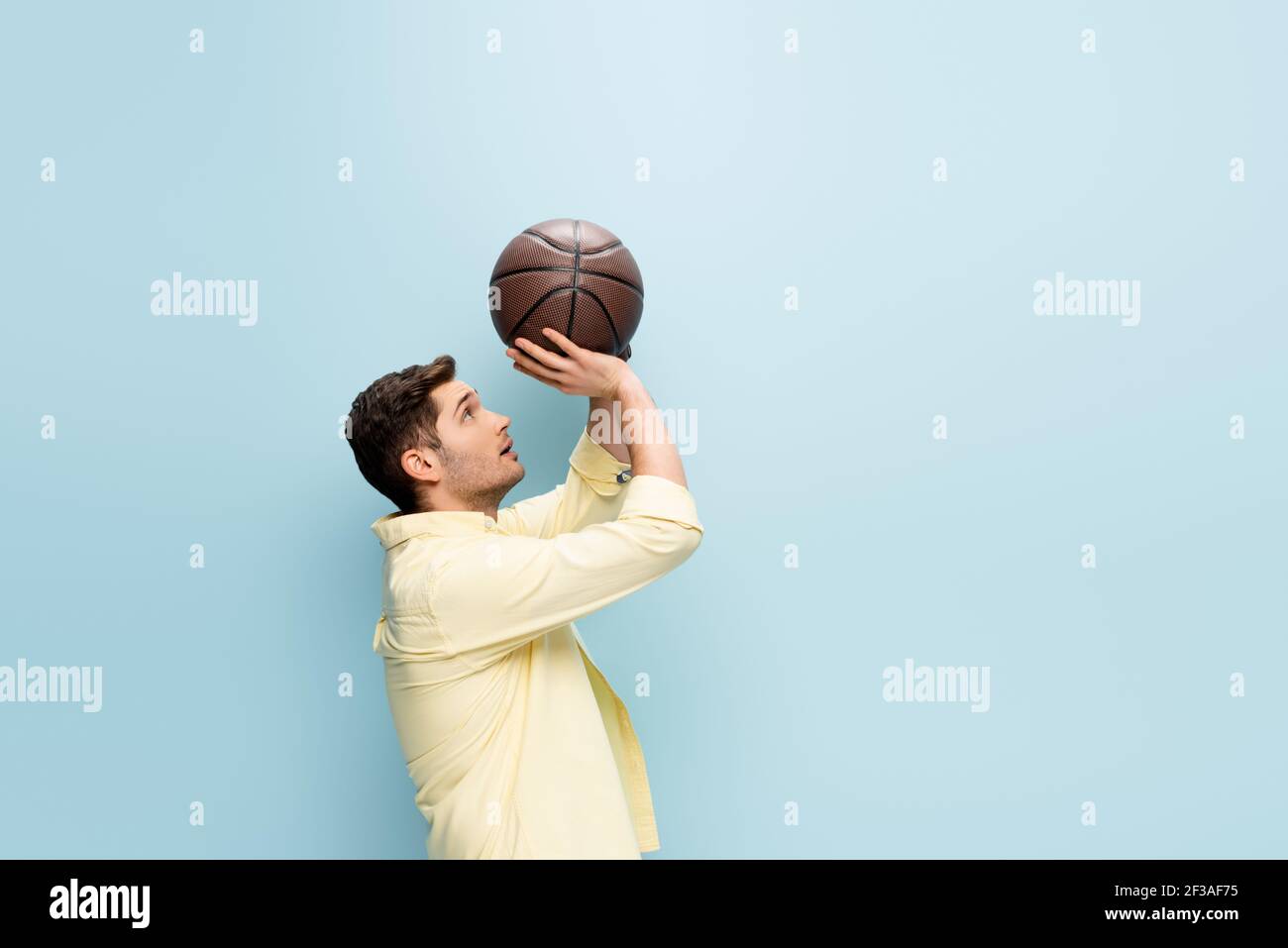 side view of man in yellow shirt throwing basketball on blue Stock ...