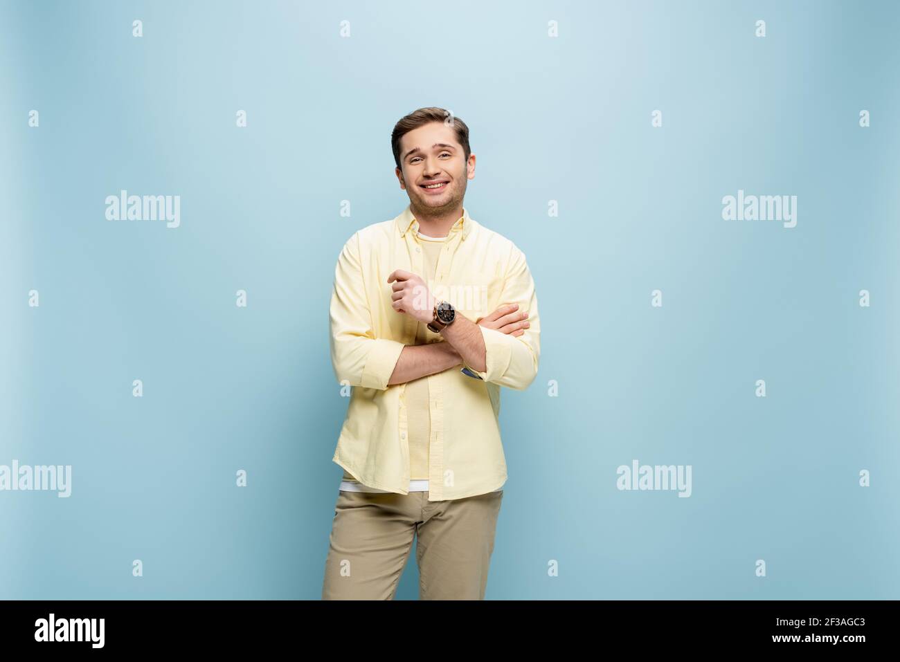 cheerful young man standing with crossed arms and smiling on blue Stock ...