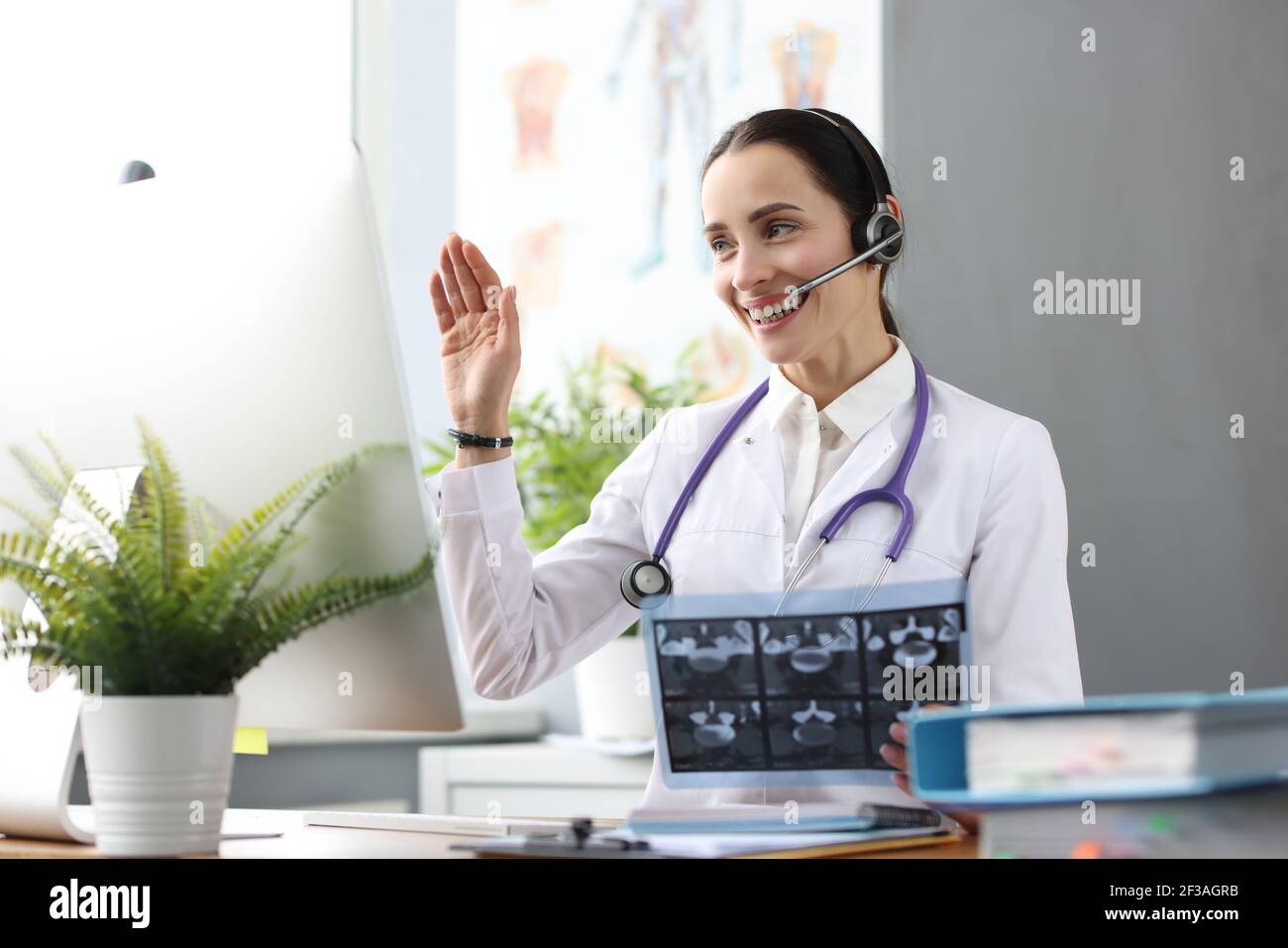 Doctor with headphones and microphone waving hand at computer screen ...