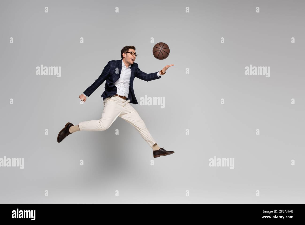 full length of cheerful businessman playing basketball while levitating ...