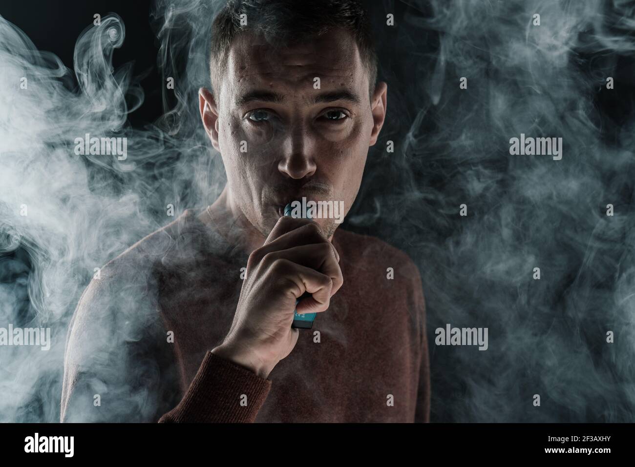 a man smokes a vape on a black background white smoke steam portrait ...